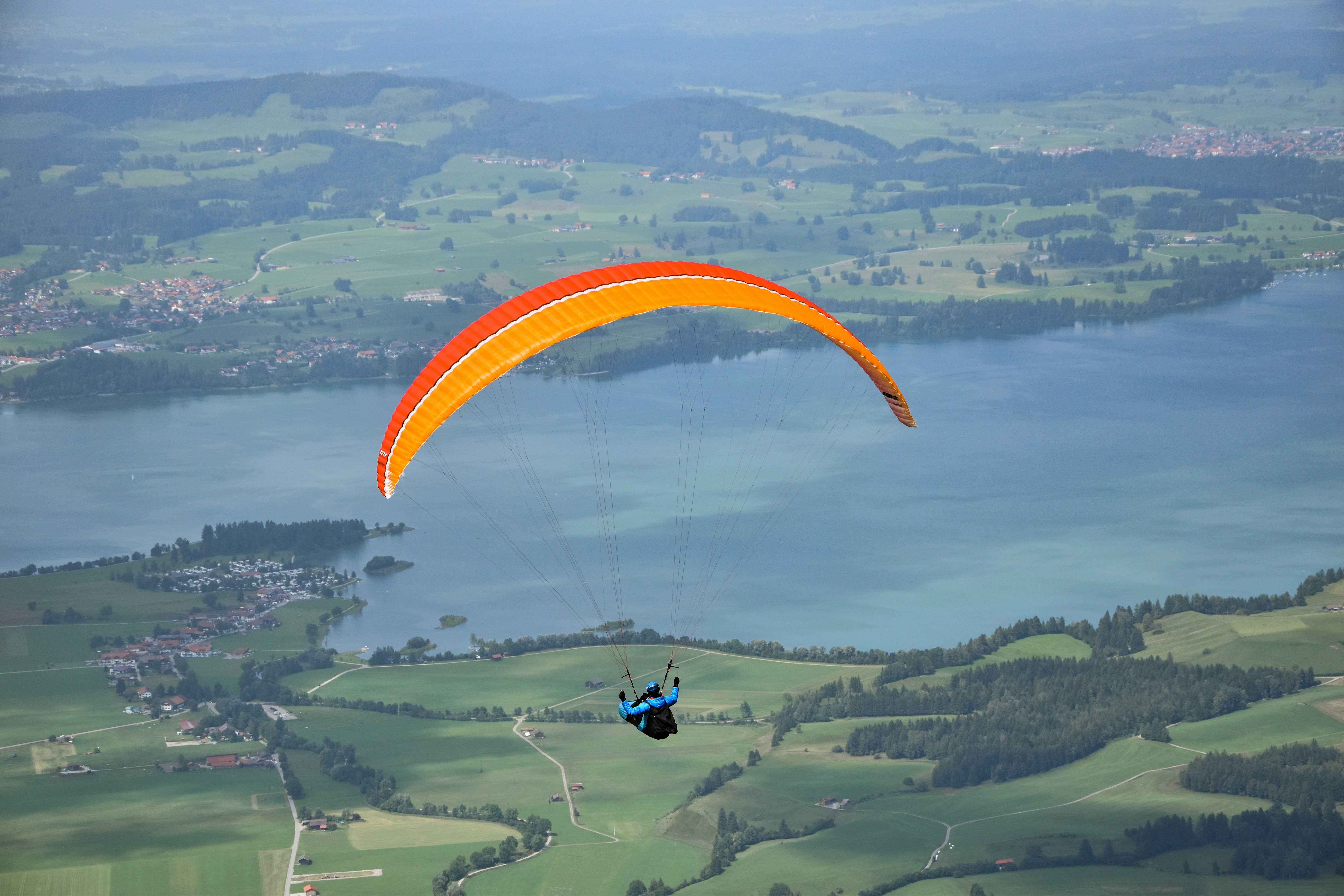 Amber Paraglider Traces an Orange Ribbon Over a Lake-Valley Panorama