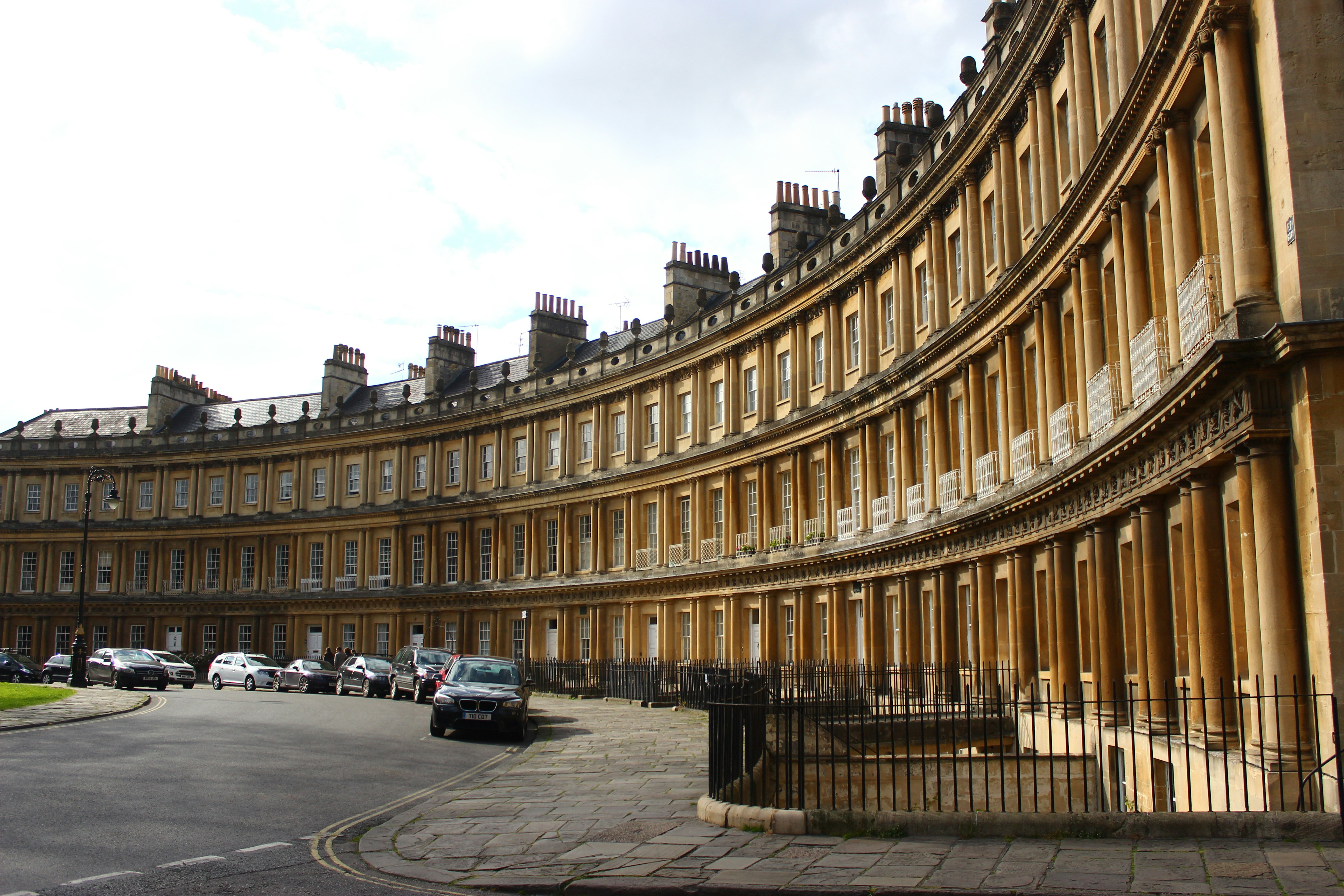Historic curved building with parked cars along a quiet street under a partly cloudy sky.