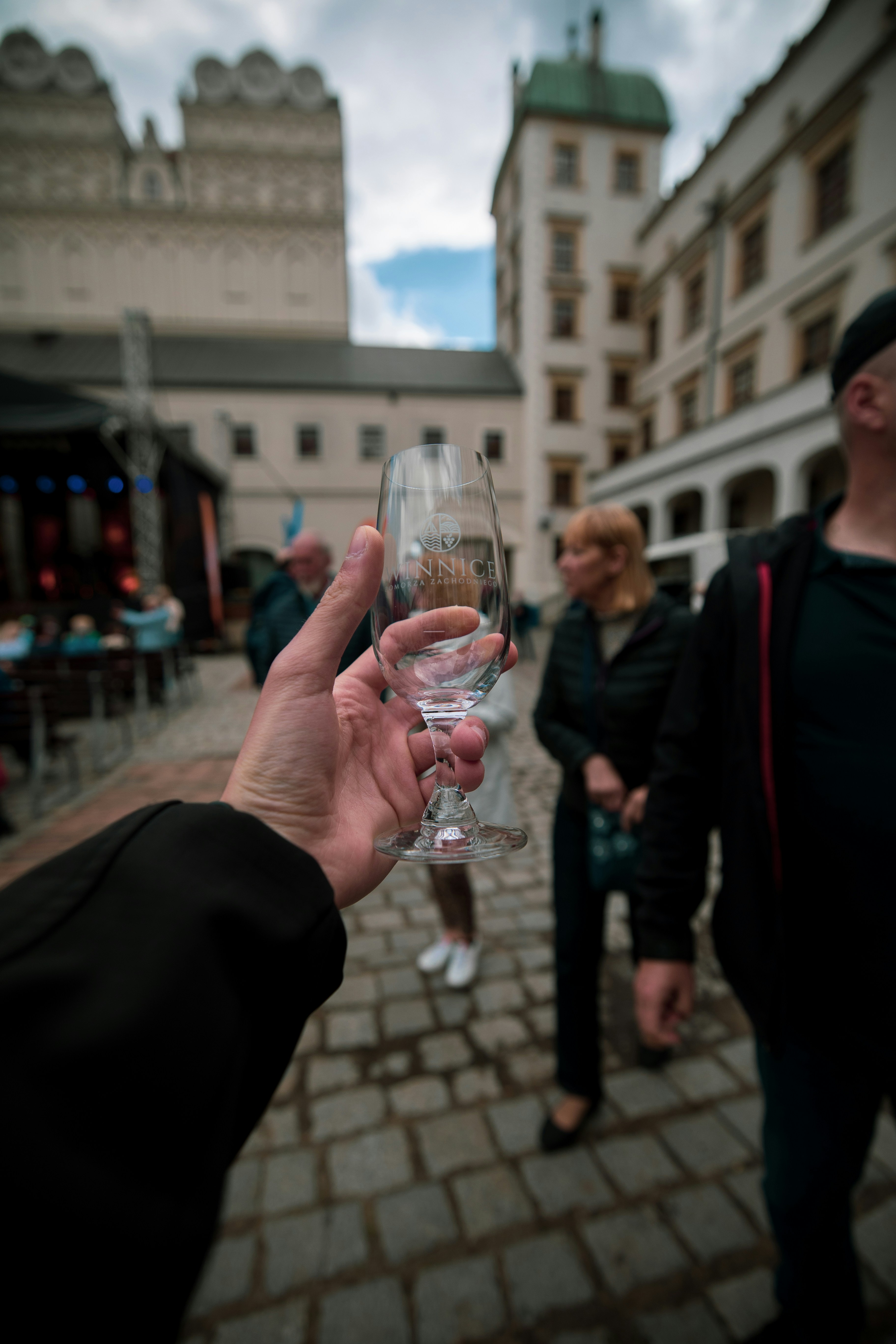 Toast in Focus: A Handheld Glass Framed Against a Stately Courtyard