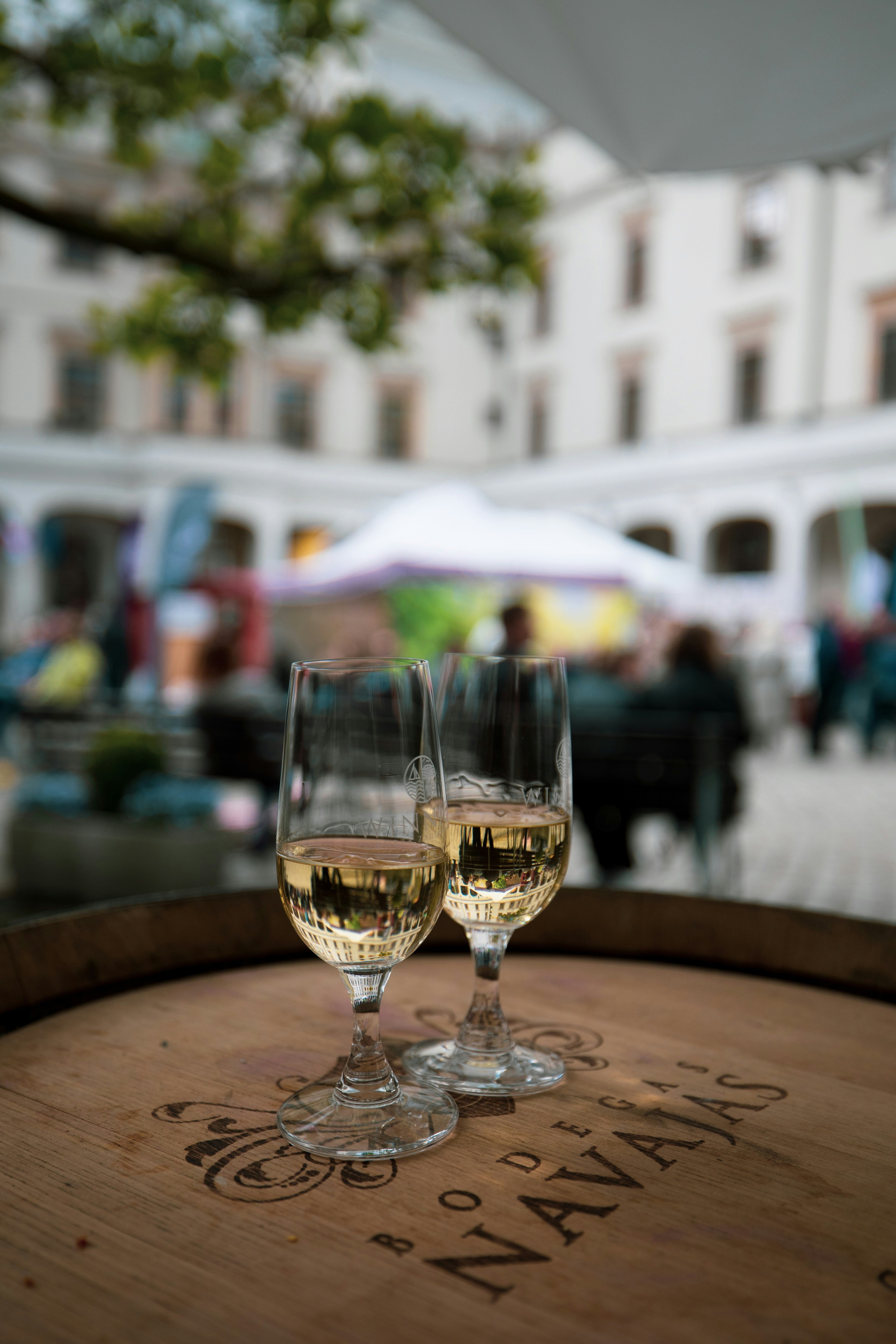 Two Glasses of White Wine on a Wooden Barrel Table at an Outdoor Courtyard Café