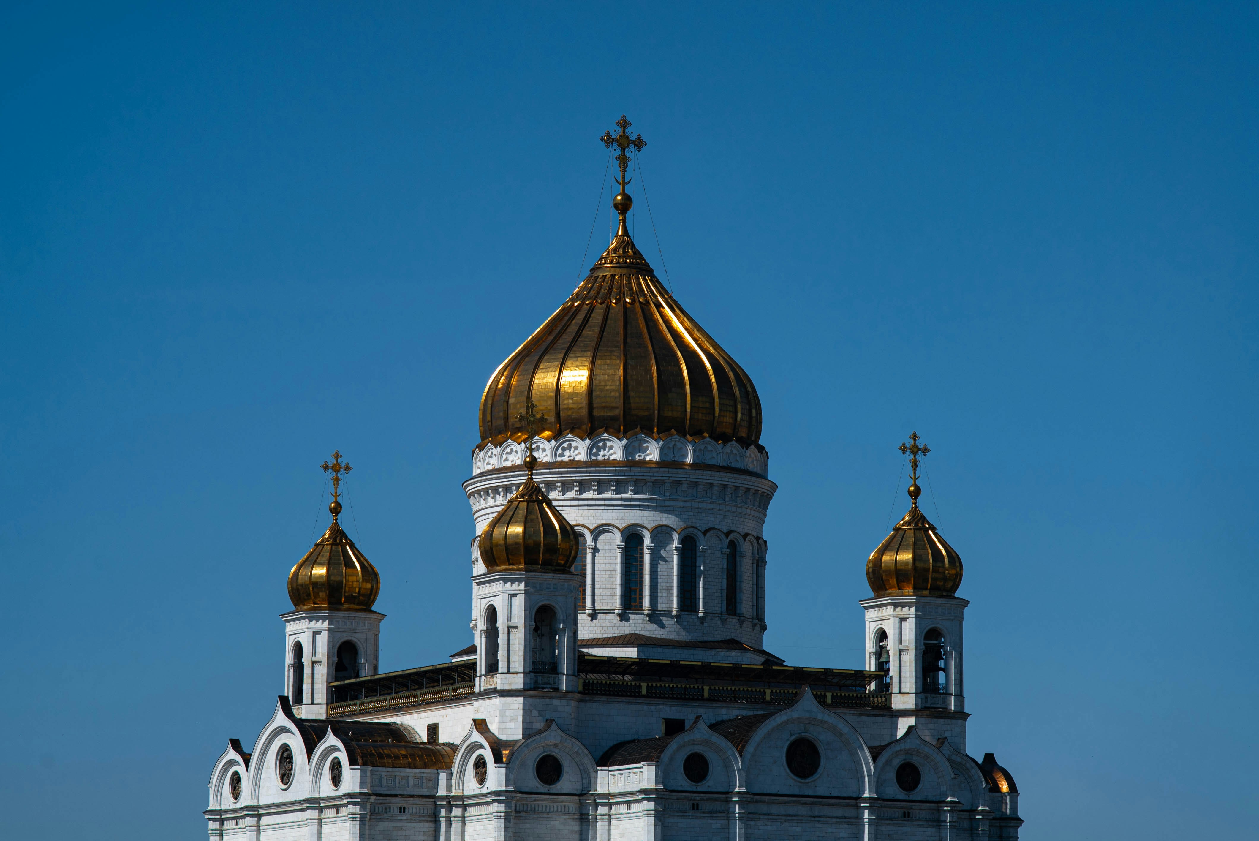 Ornate church with striking golden domes and white stone walls, set against a clear blue sky.