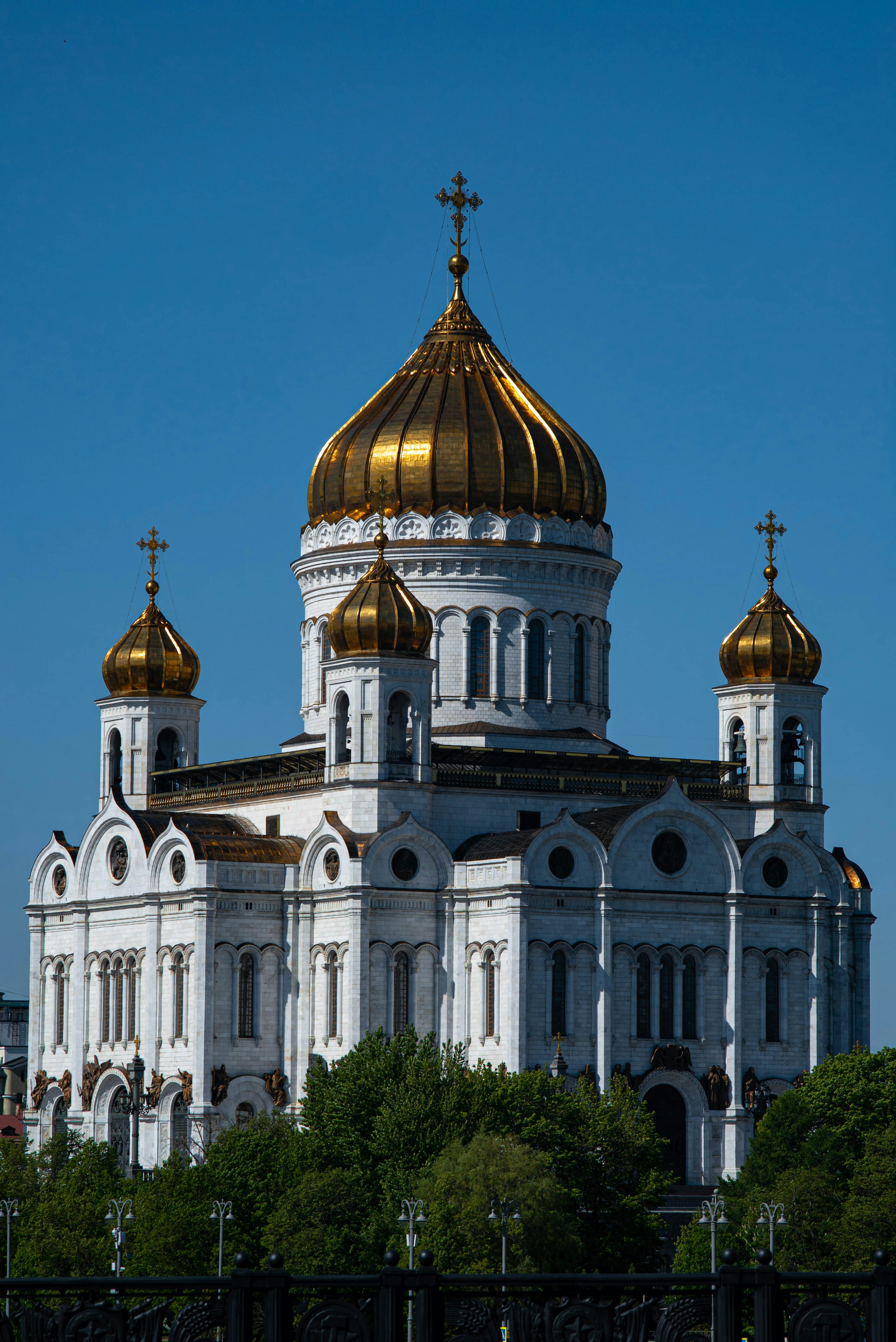 Ornate cathedral with striking golden domes and white stone façade, surrounded by lush greenery under a clear blue sky.