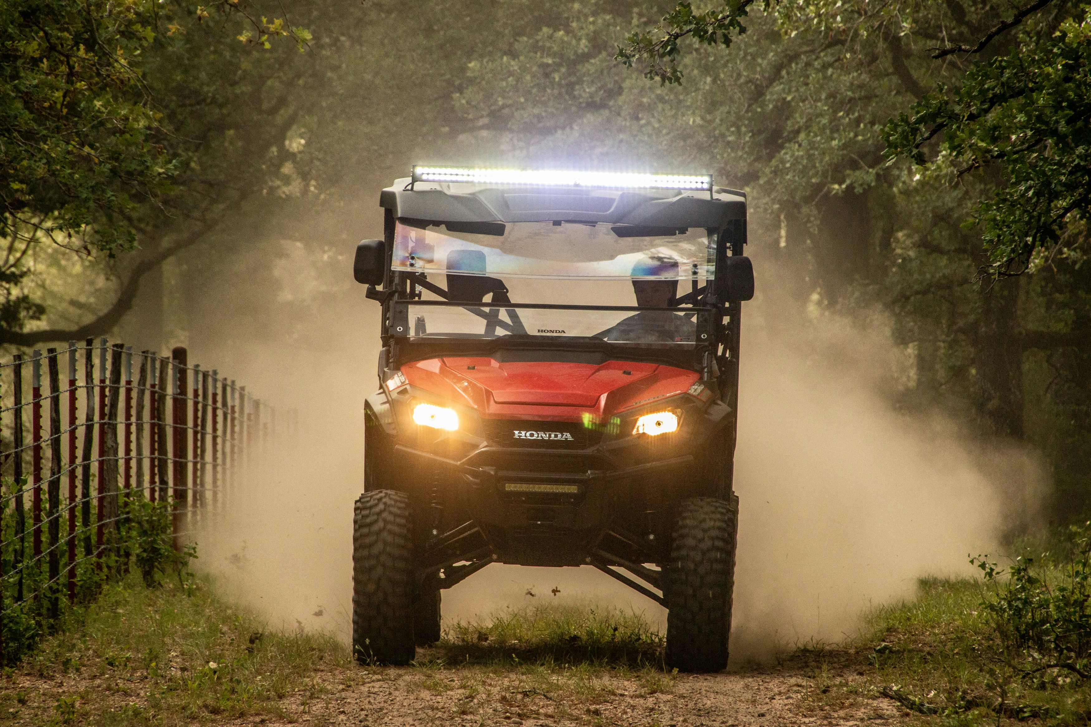 Honda UTV navigating a dusty trail surrounded by trees, showcasing rugged terrain and adventure spirit.