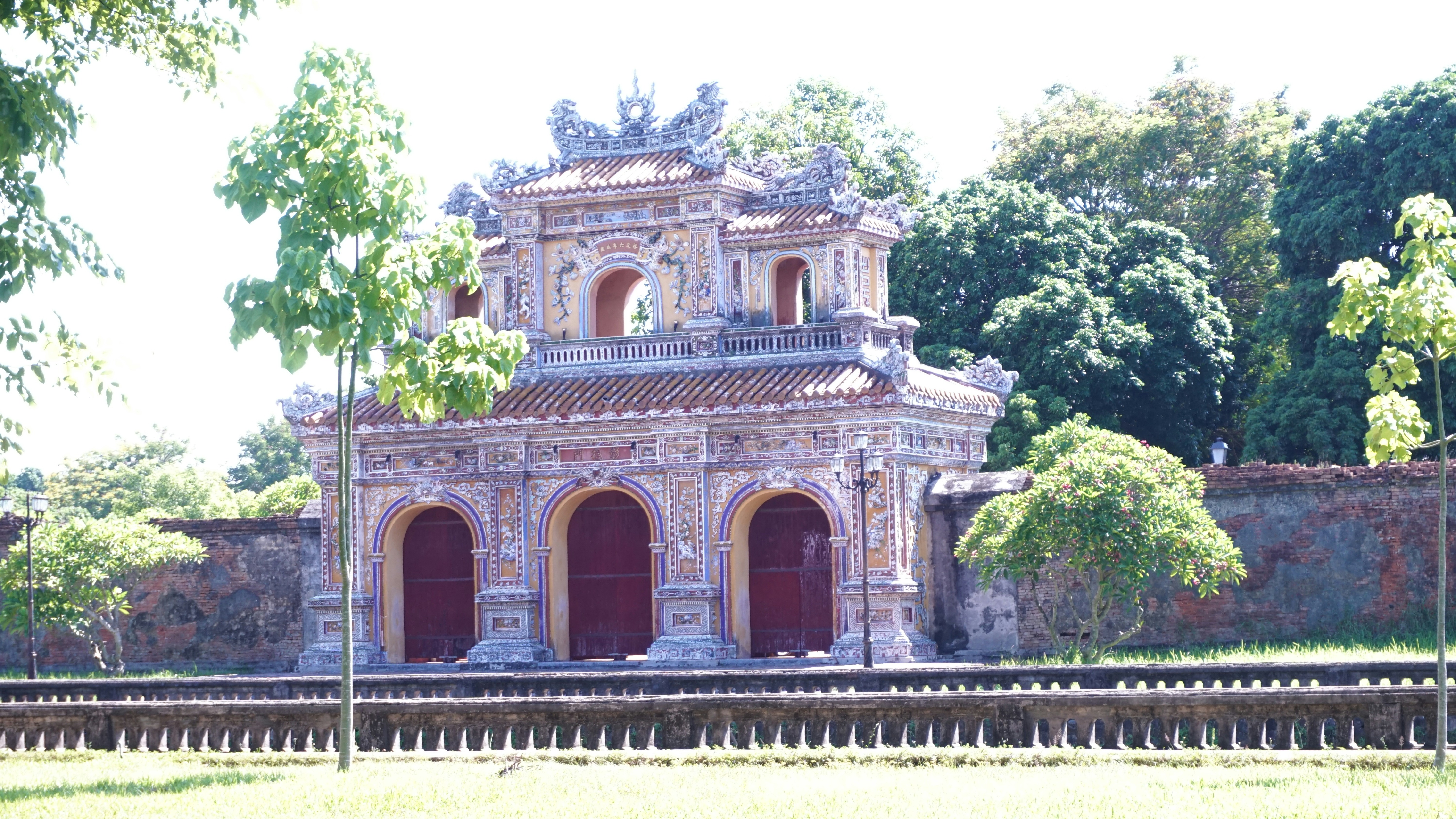 Intricate architectural structure adorned with colorful tiles, set against a lush green backdrop in Huế, Vietnam.