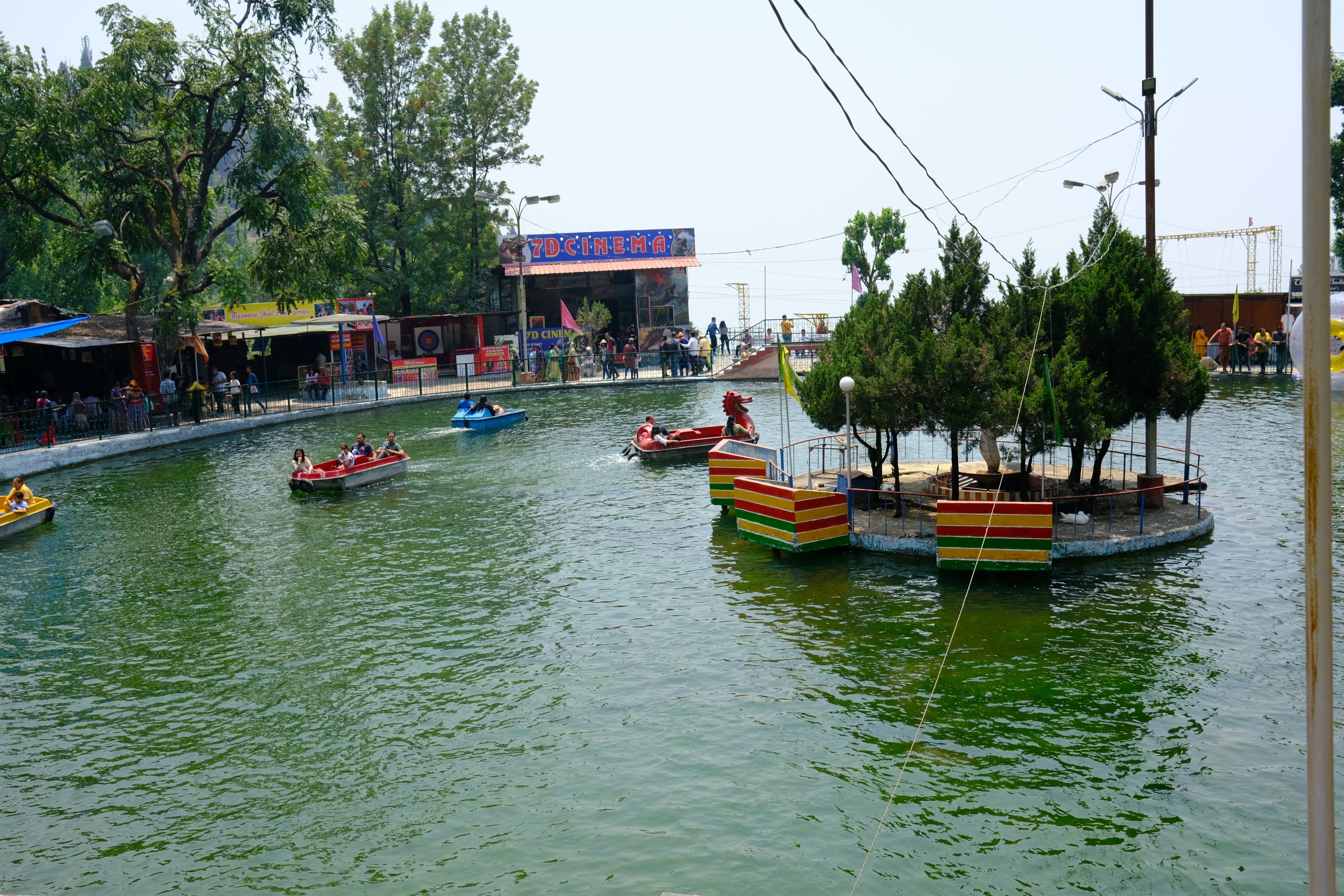 Colorful paddleboats gliding across a serene lake, surrounded by greenery and a lively amusement area.