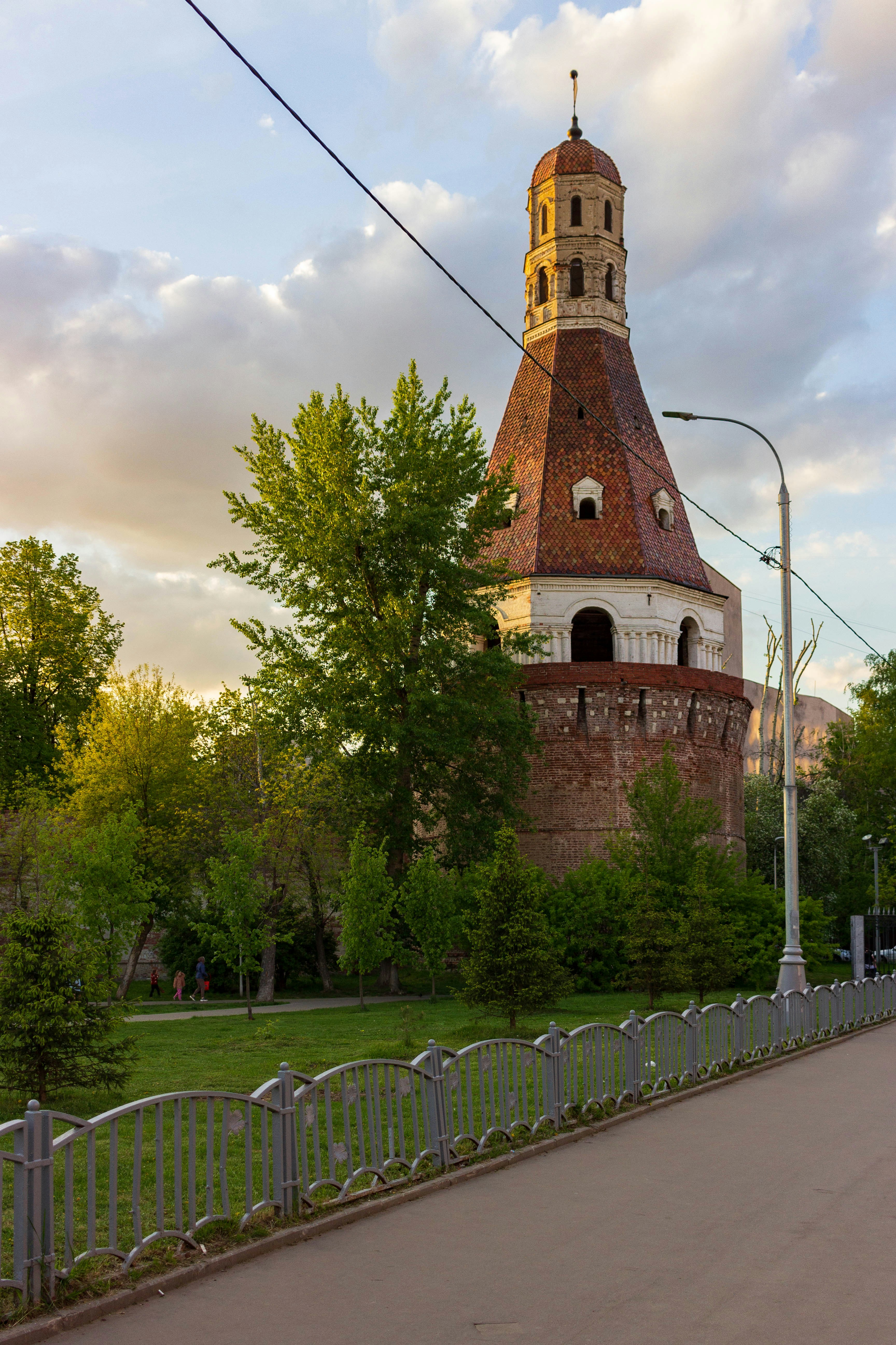 Historic tower surrounded by lush greenery and a peaceful pathway, showcasing the blend of architecture and nature.