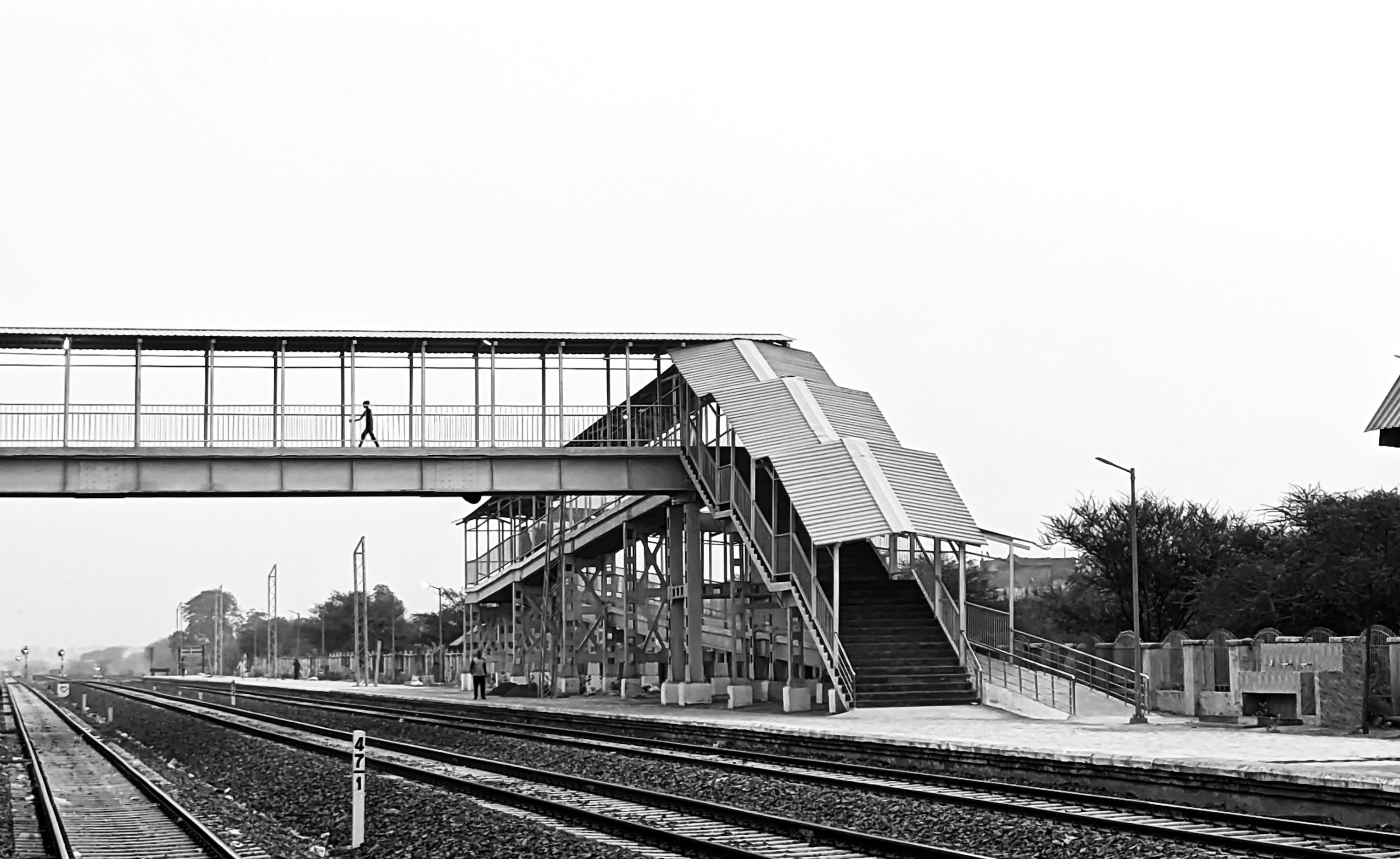 Black and white view of a deserted train station with a footbridge and tracks extending into the distance.