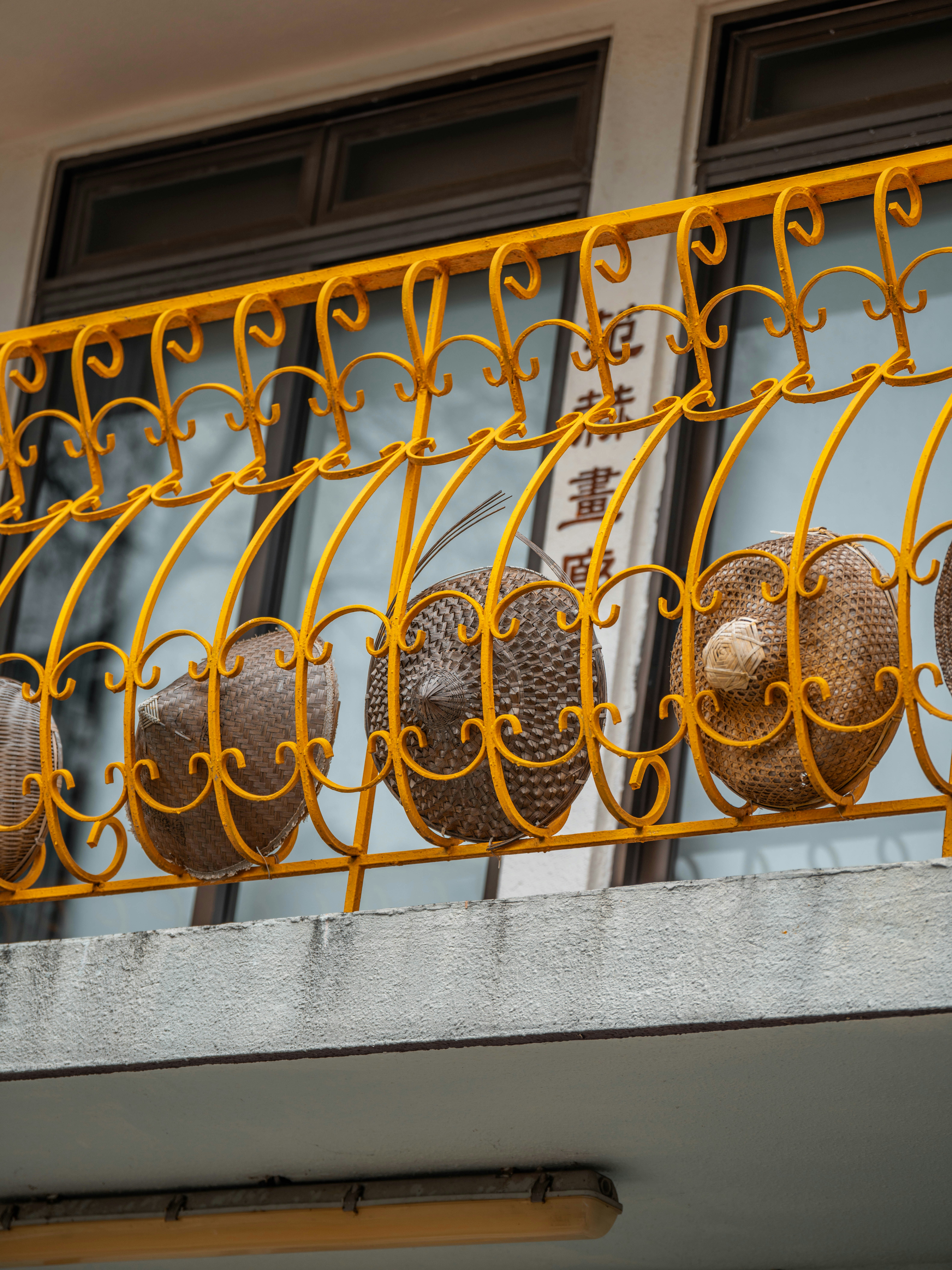 a balcony with a yellow iron railing and a number of hats hanging on it
