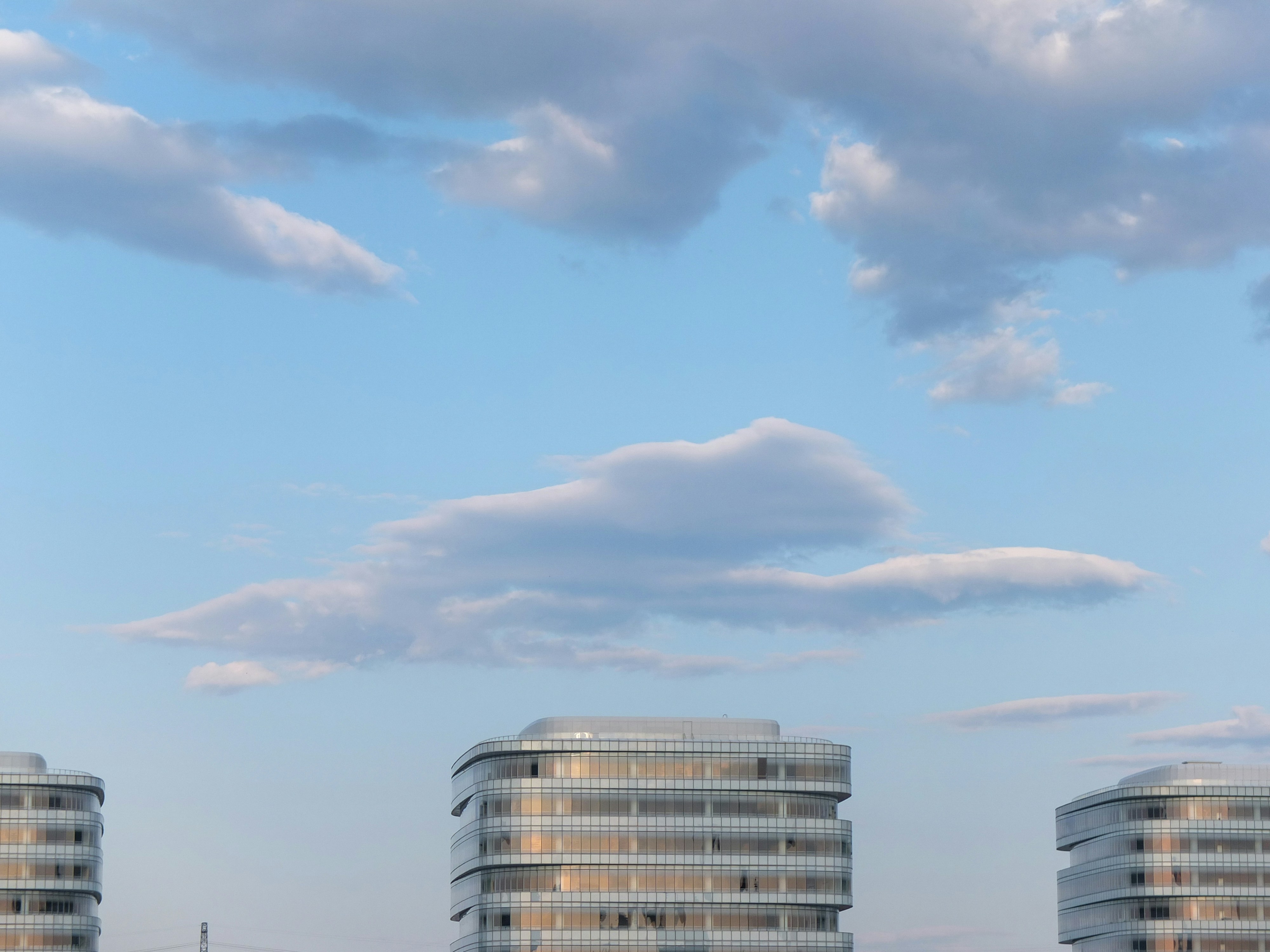 Three modern buildings reflect soft hues of the sky, framed by gentle clouds. The architectural design emphasizes smooth curves and sleek lines.