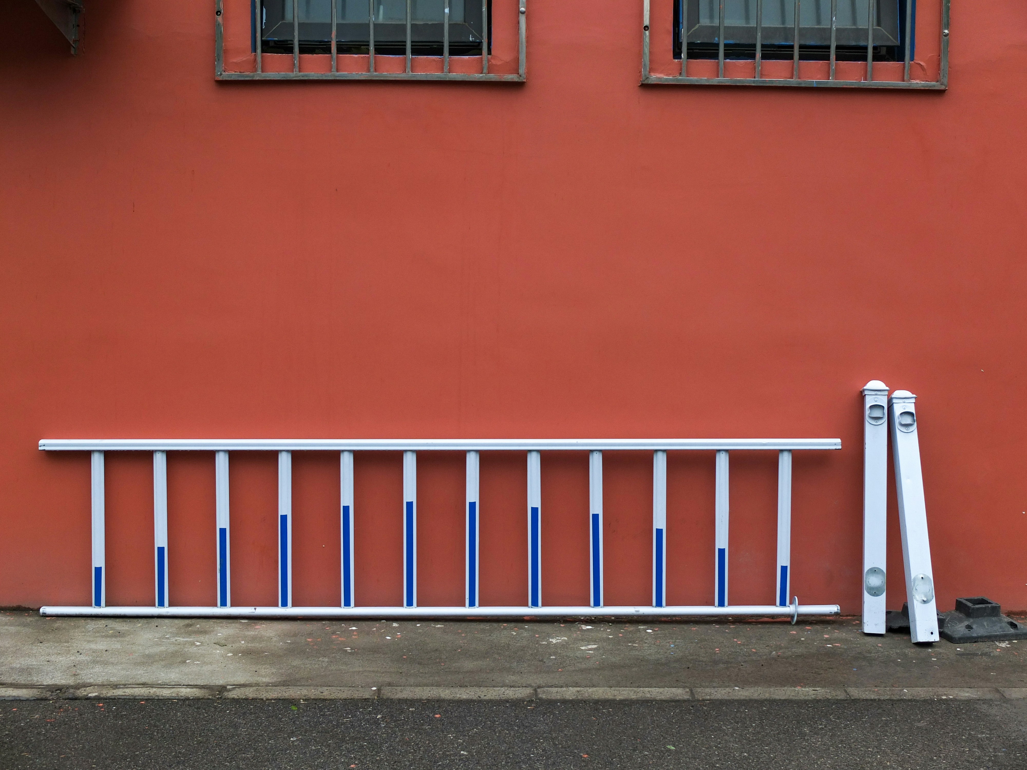 A series of white and blue painted poles arranged against a vibrant red wall, showcasing an intriguing interplay of shapes and colors.