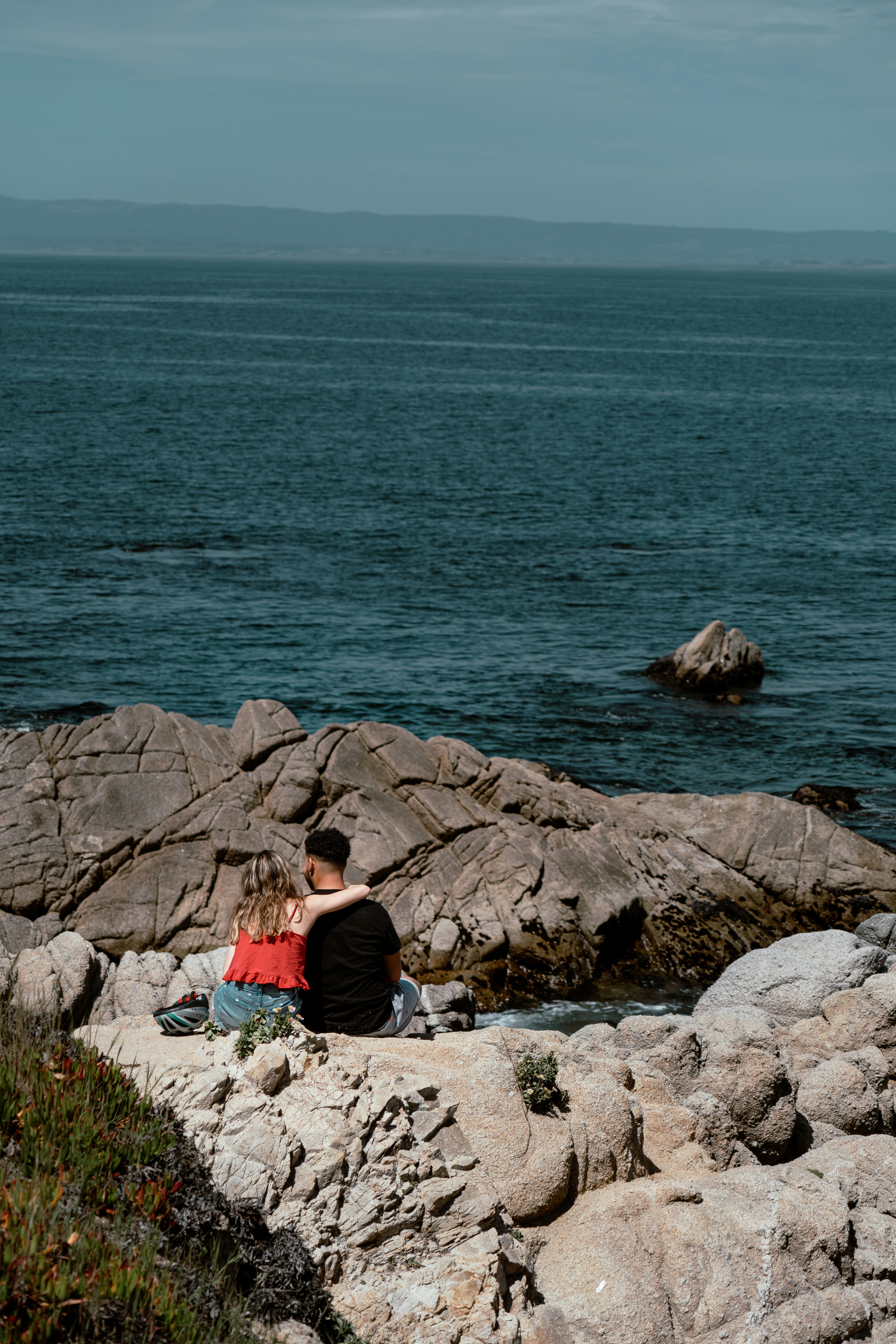 a man and a woman sitting on rocks near the ocean