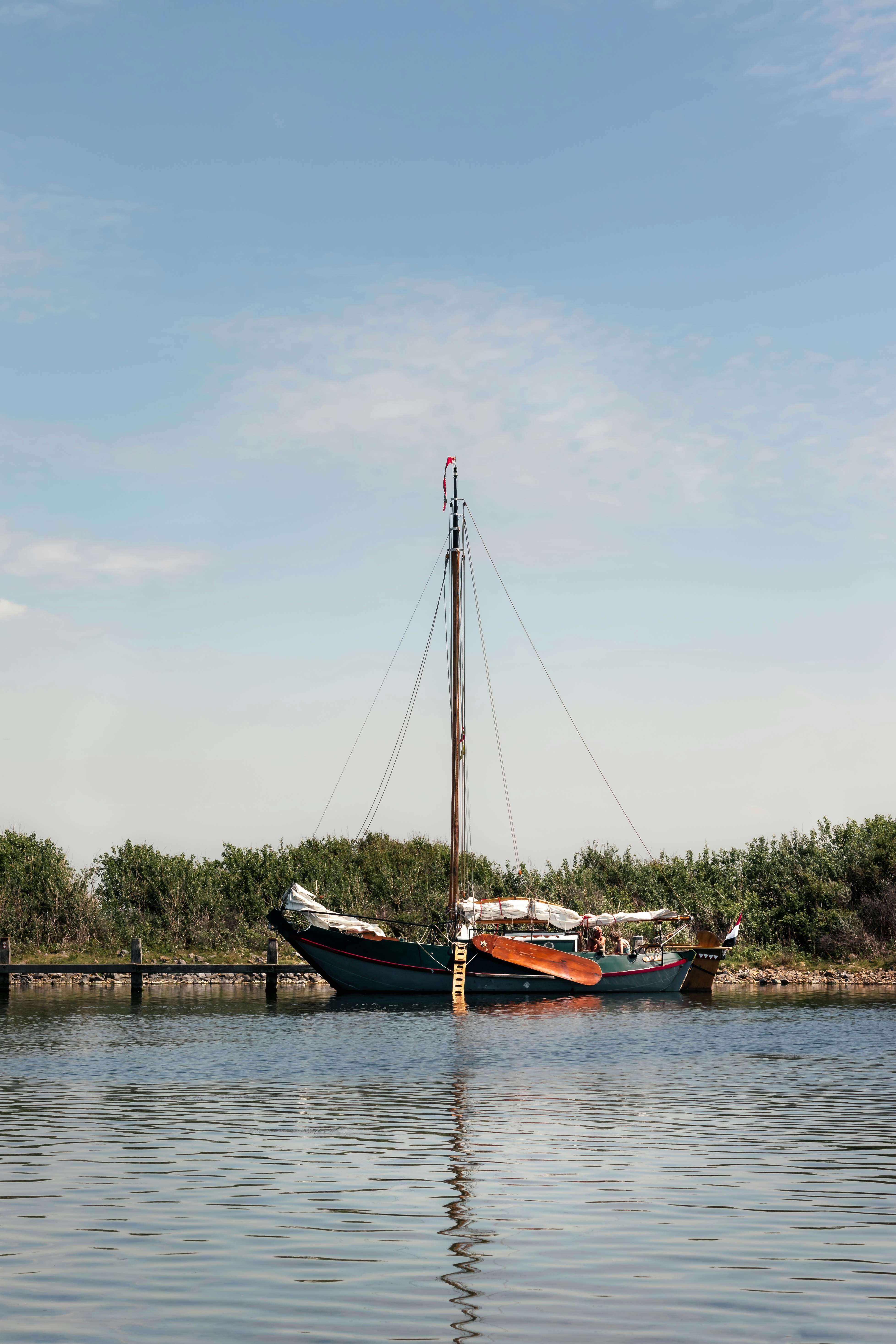 A traditional sailing boat anchored peacefully in a calm harbor, surrounded by lush greenery and a clear blue sky.