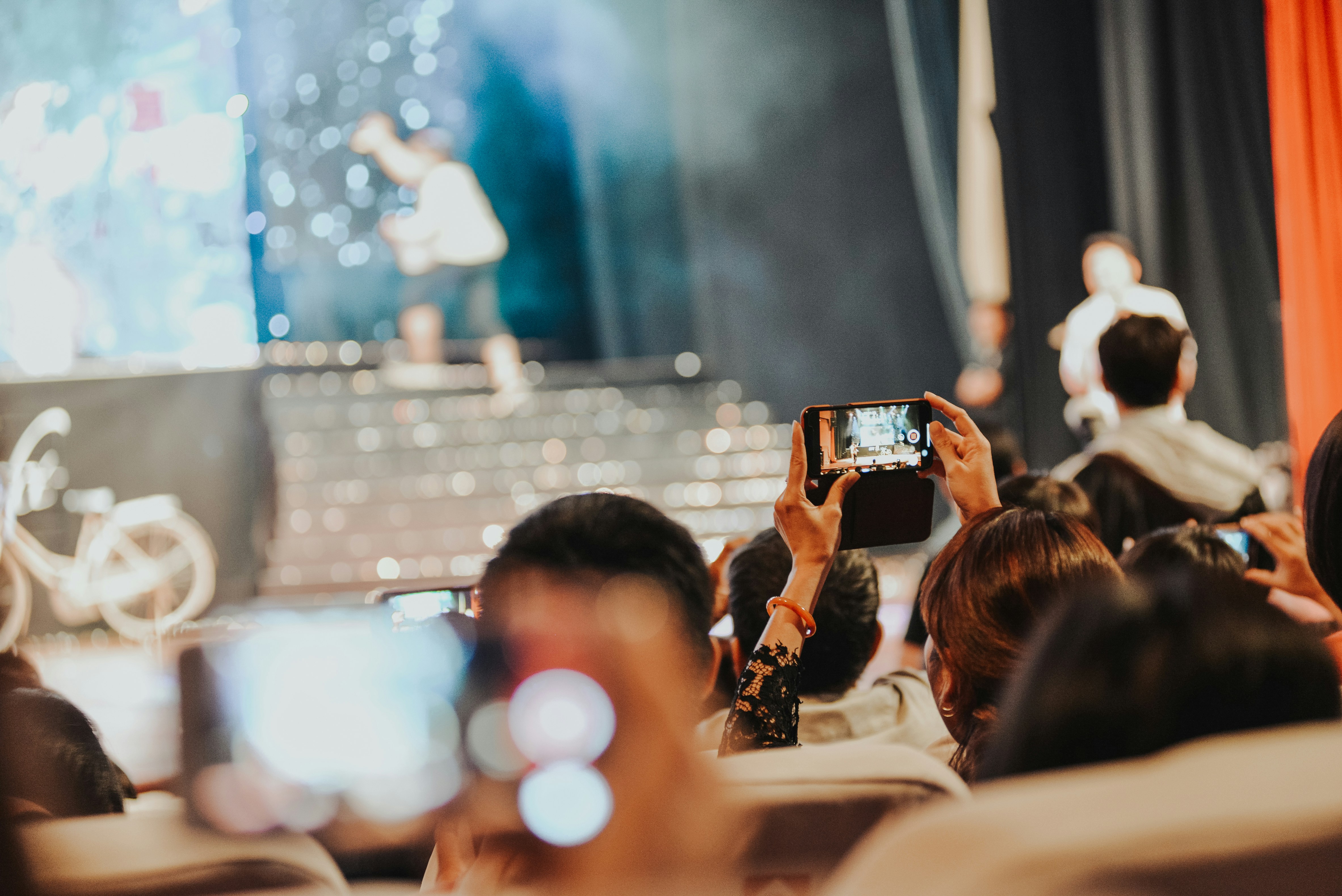 Audience members photographing a stage performance, with bokeh lights creating a vibrant backdrop.