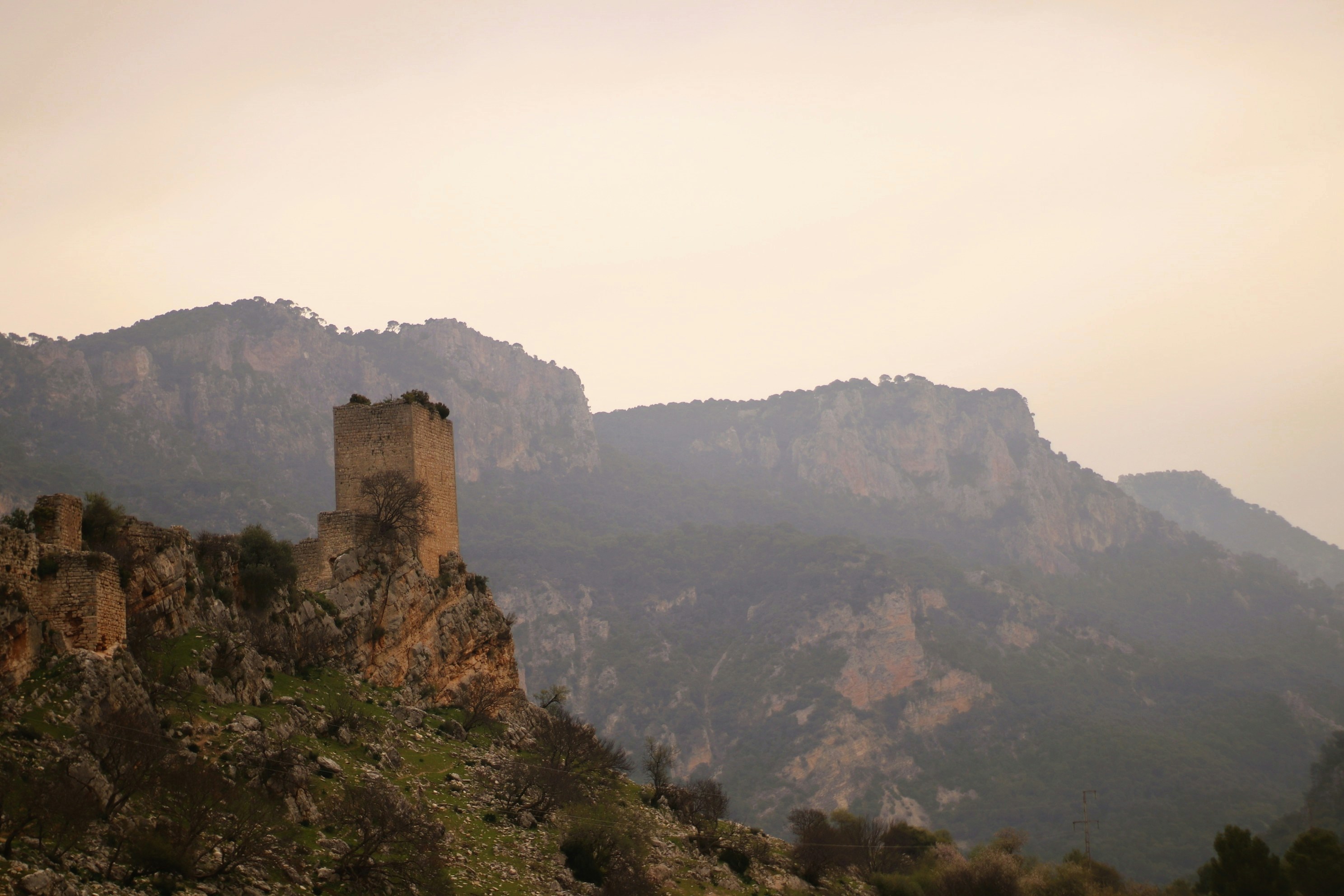 Old stone tower perched on a rugged hillside with mist-covered mountains in the background.