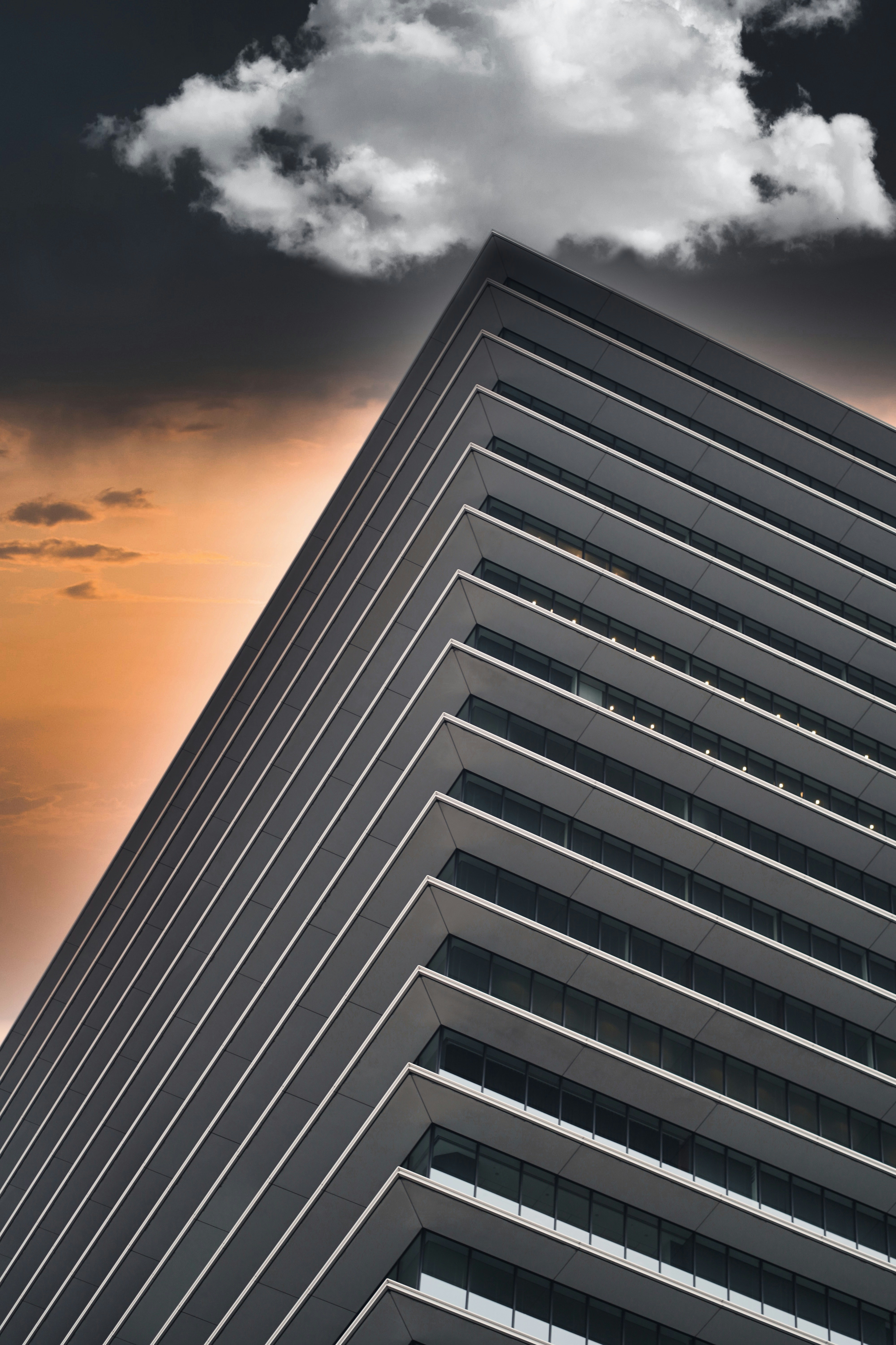 Angular building facade converging towards a dramatic sky with layered clouds at sunset.
