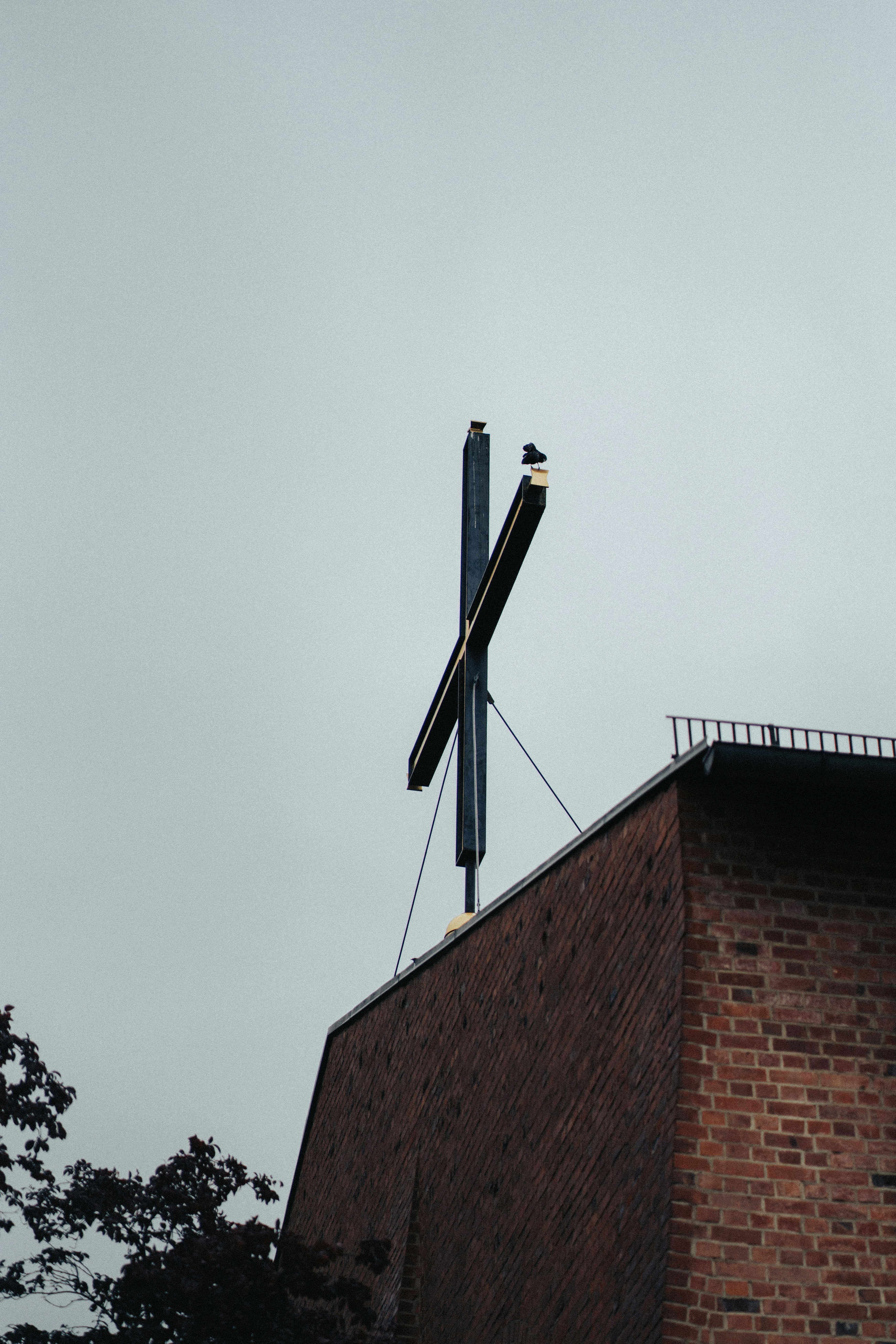 Rooftop Sign Rising: A solitary crossbeam over brickwork against a pale sky