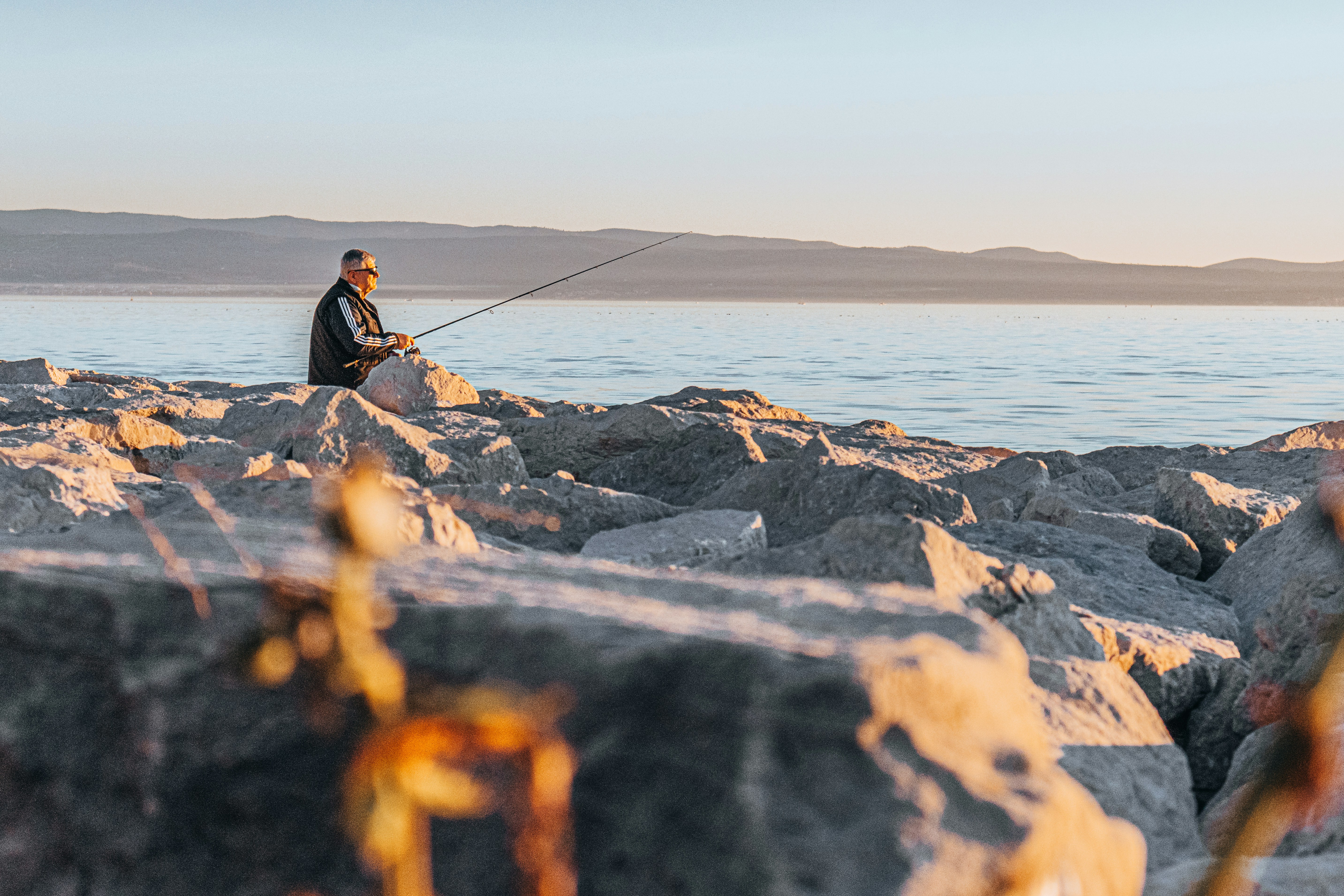 Foto Un hombre sentado en las rocas pescando en un lago – Imagen ...