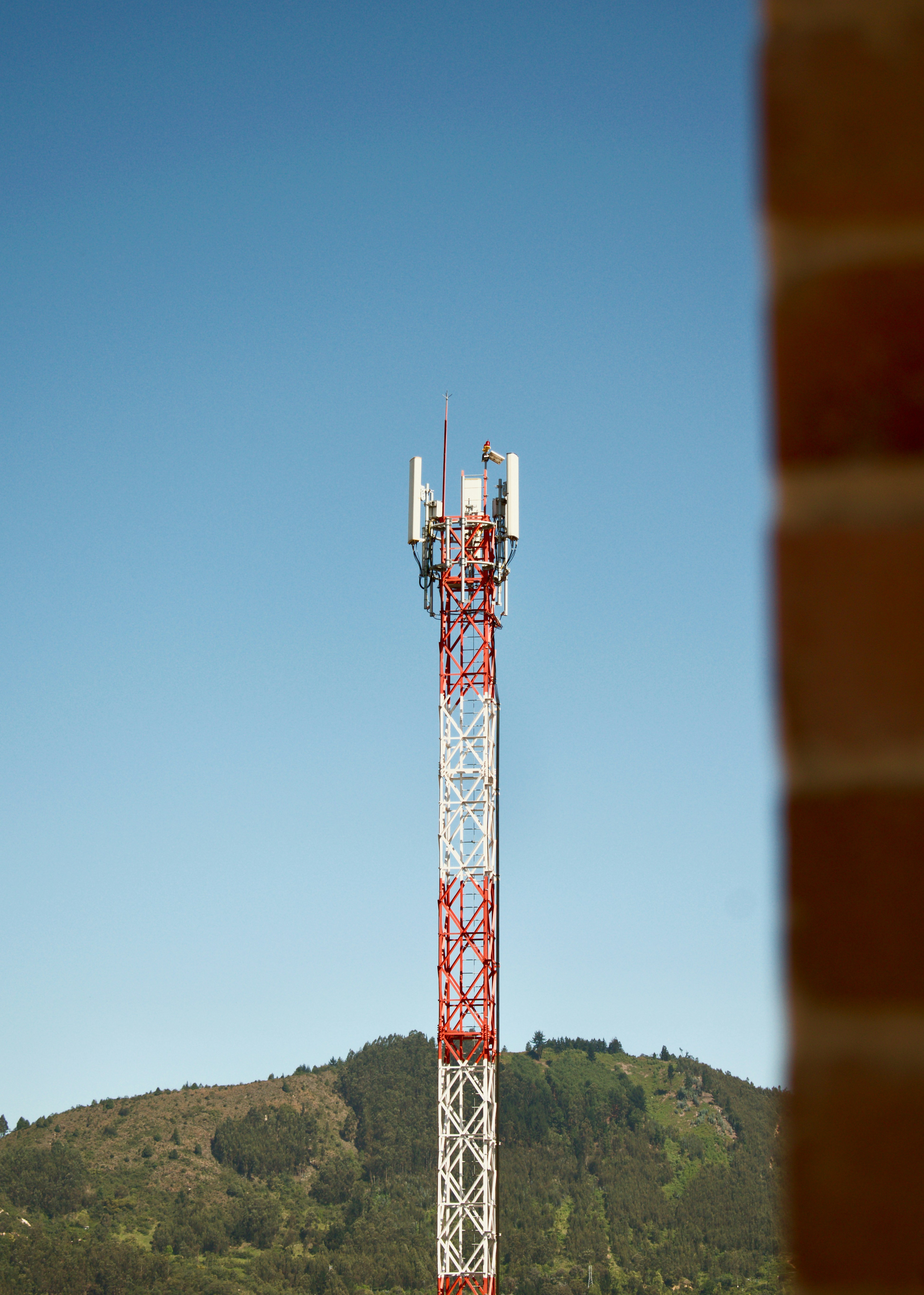 Vertical Sentinel Over the Hills: A Red-and-White Telecom Tower Reaches Toward the Sky