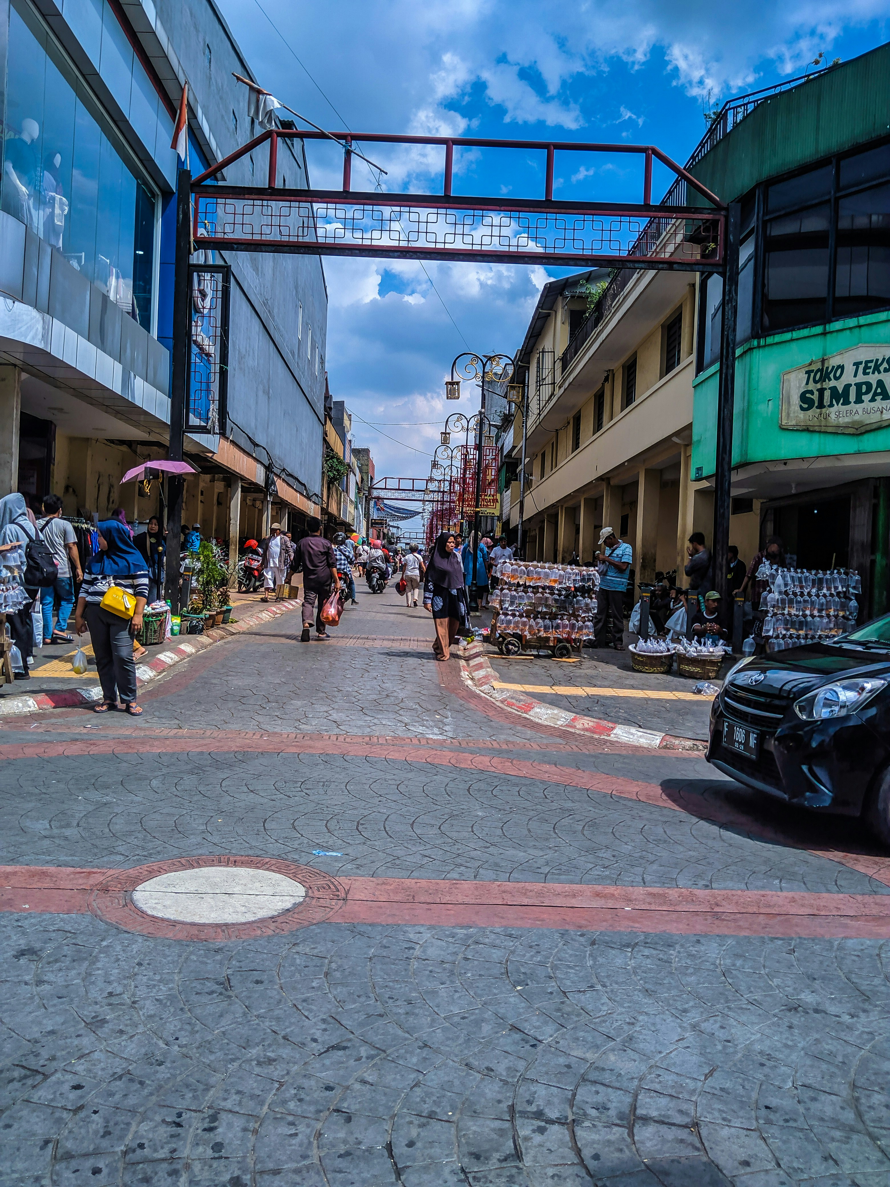 Sunlit Market Lane: Pedestrians and Vendors Traverse a Colorful Street