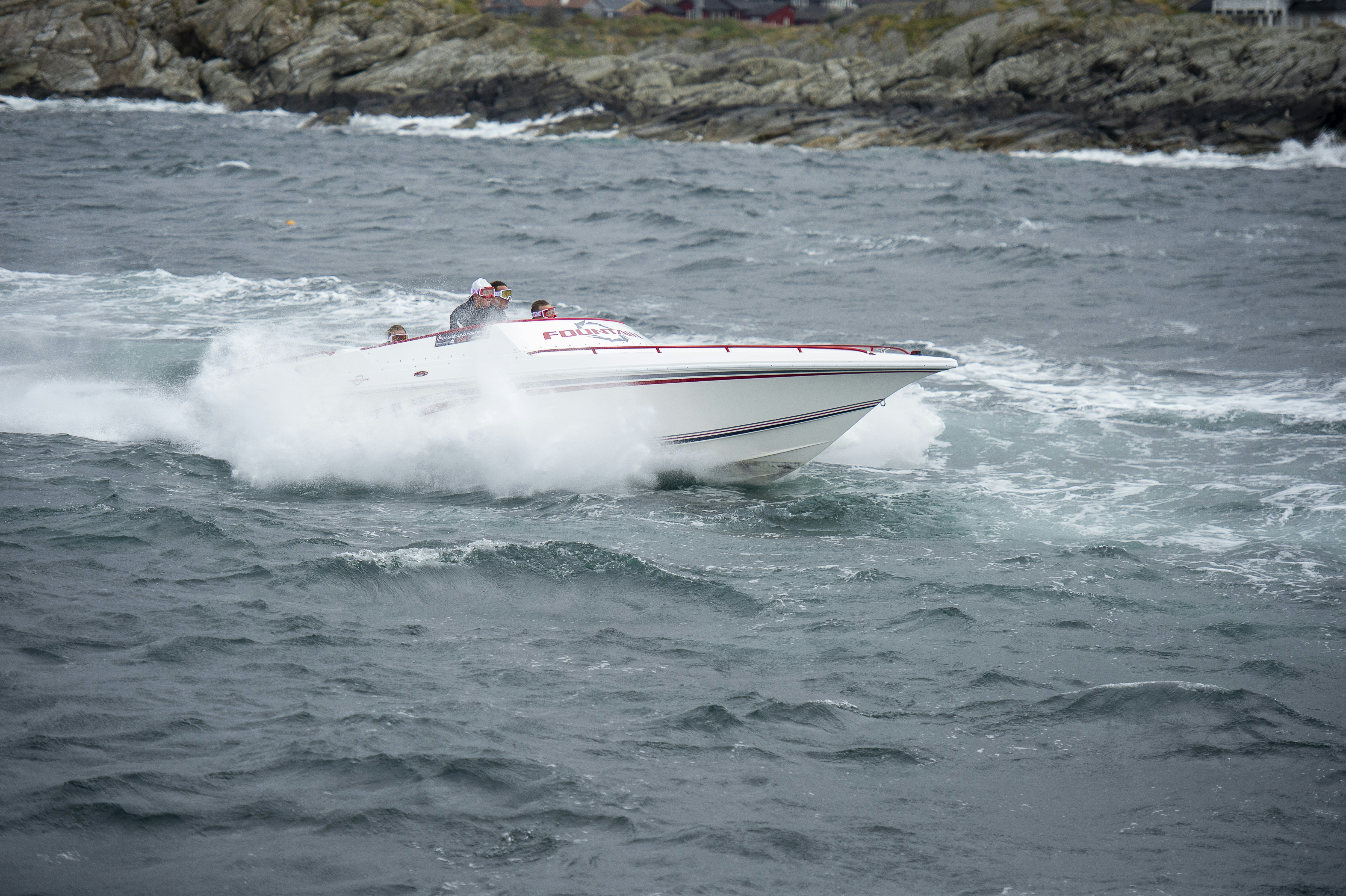A speed boat speeds through the water near a rocky shore photo – Free ...
