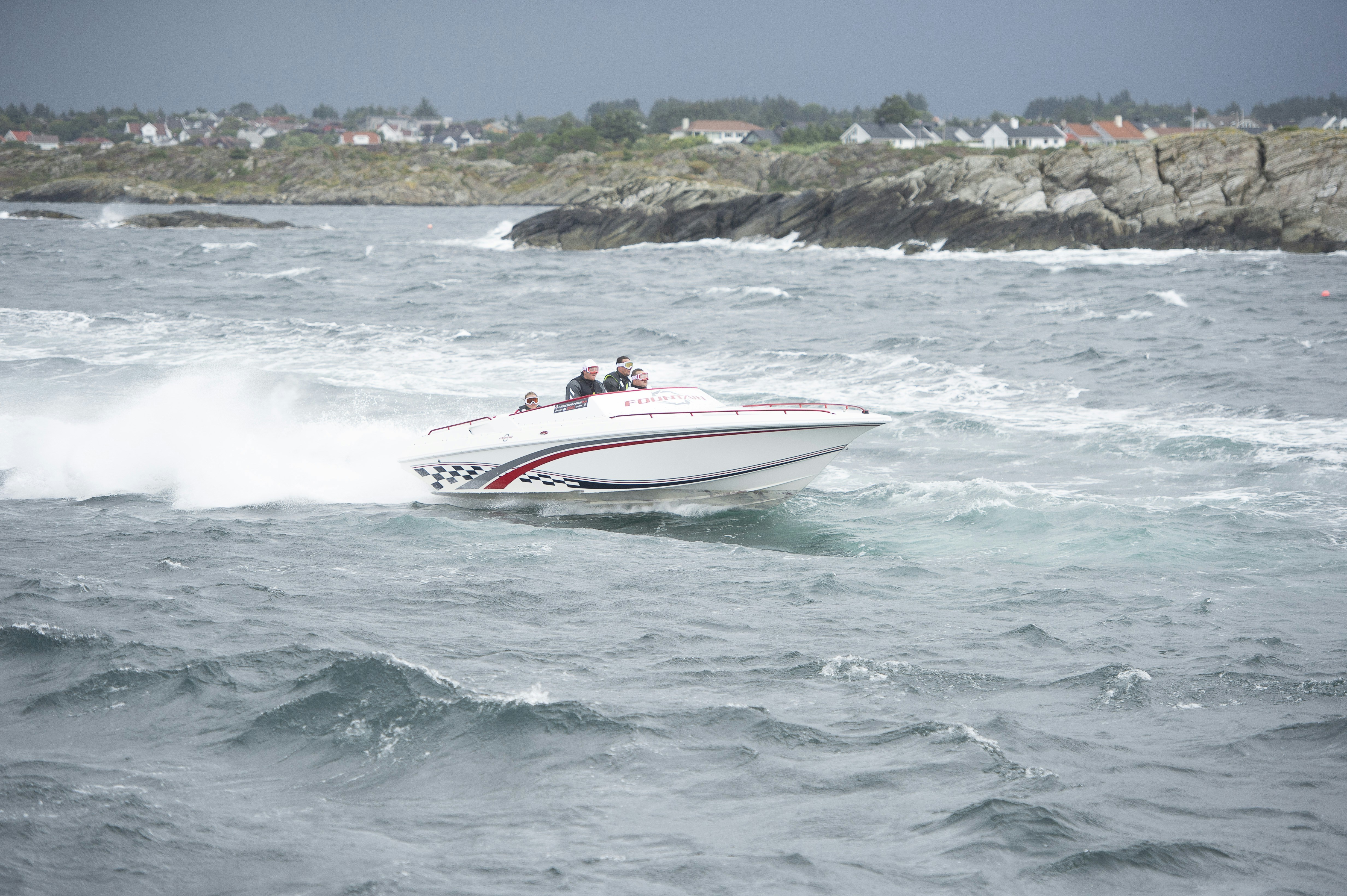 A speed boat speeds through the water near a rocky shore photo – Free ...