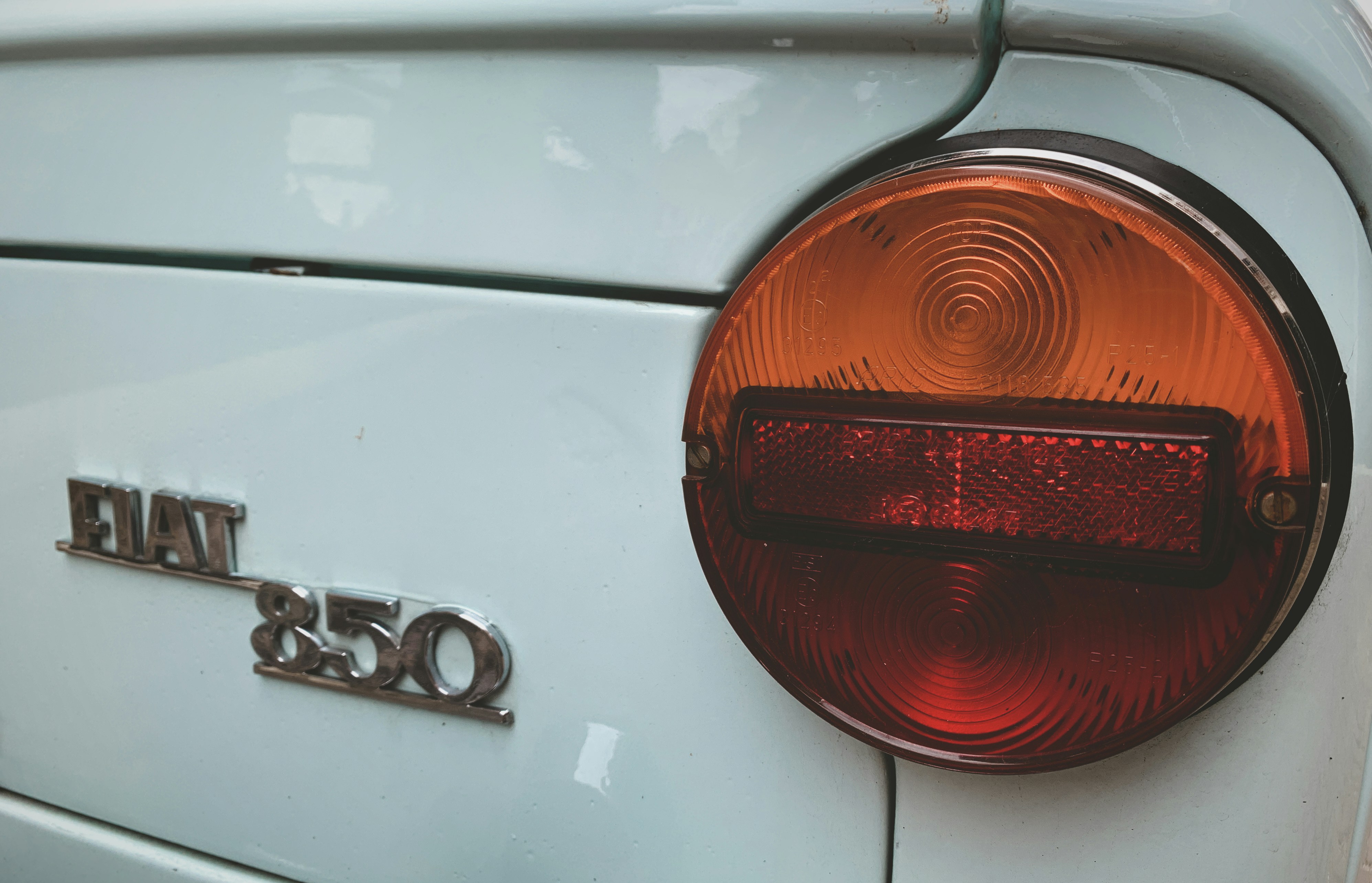 Close-up of a Fiat 850's tail light, showcasing its vintage design and distinctive color scheme. The car's badge adds a touch of nostalgia.
