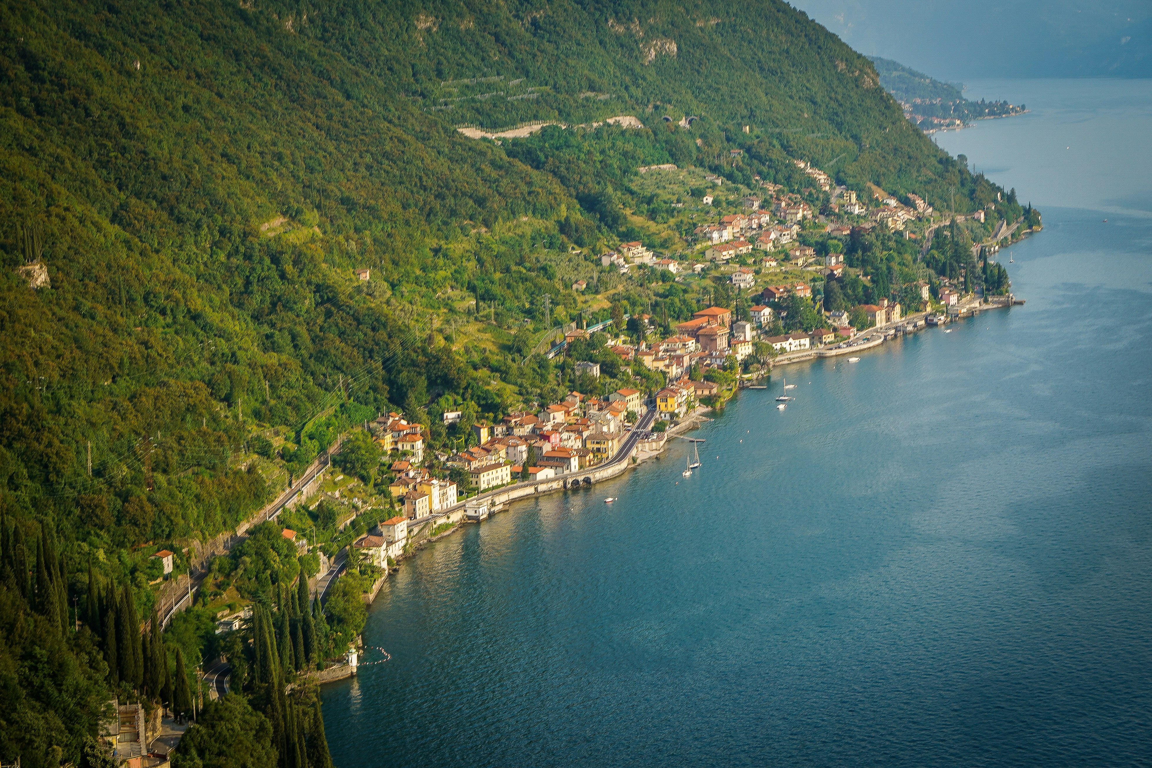 Aerial view of a quaint lakeside village nestled between lush green mountains and a tranquil blue lake.