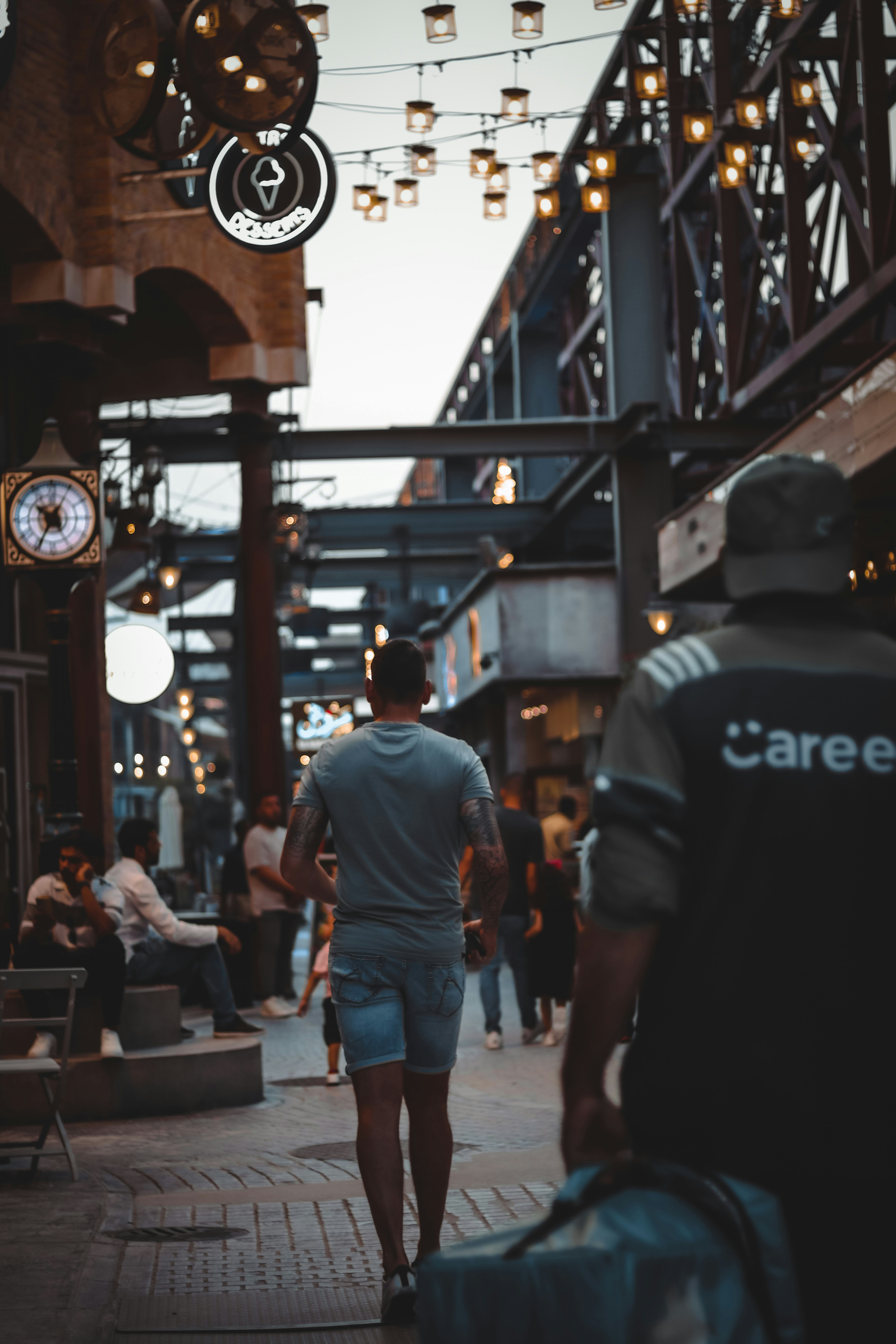 Evening Stroll Under Amber String-Lights in a Busy Urban Arcade