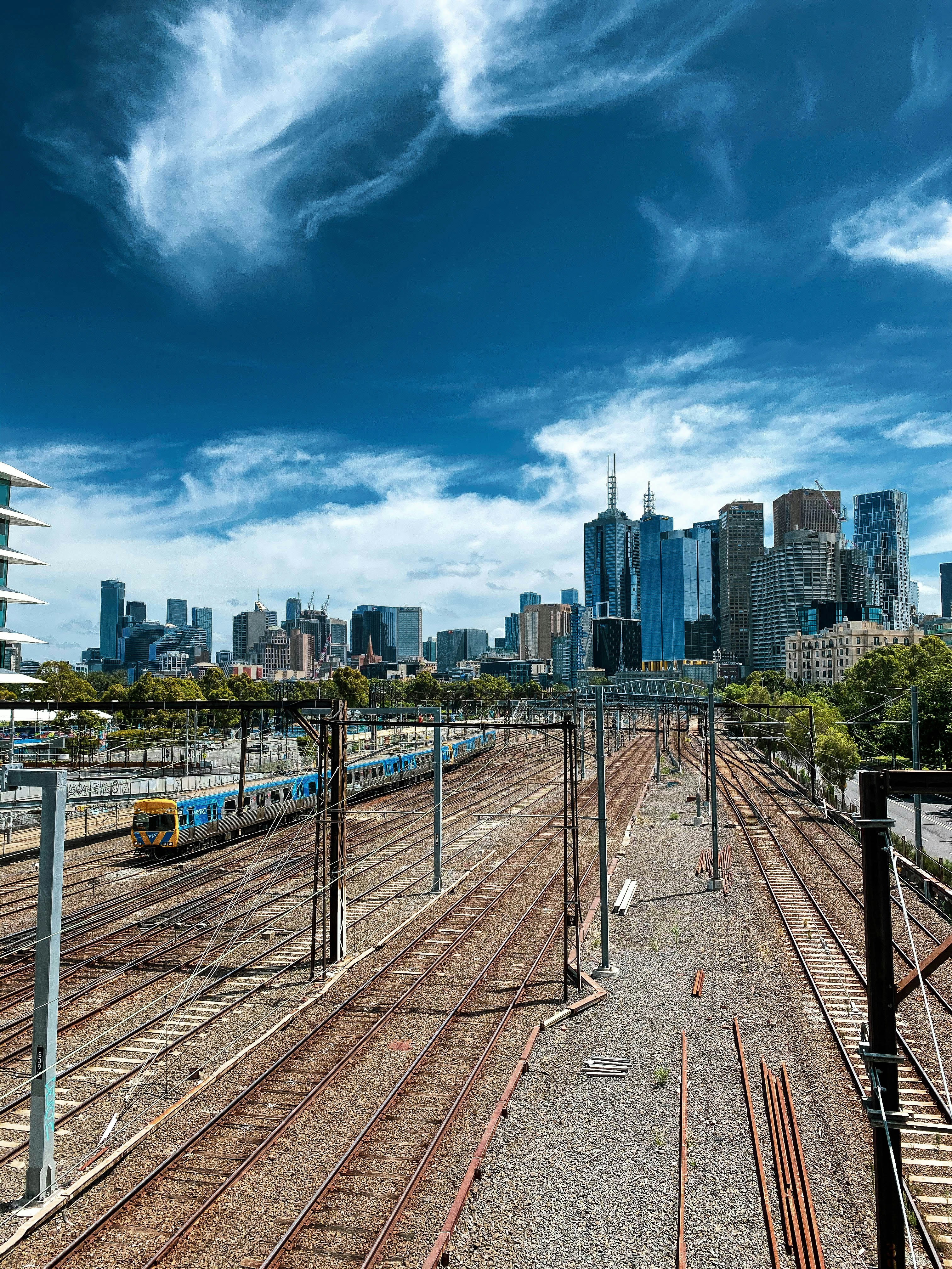 A train approaches a bustling cityscape, framed by railway tracks and vibrant blue skies. The scene captures the dynamic relationship between urban transit and modern architecture.