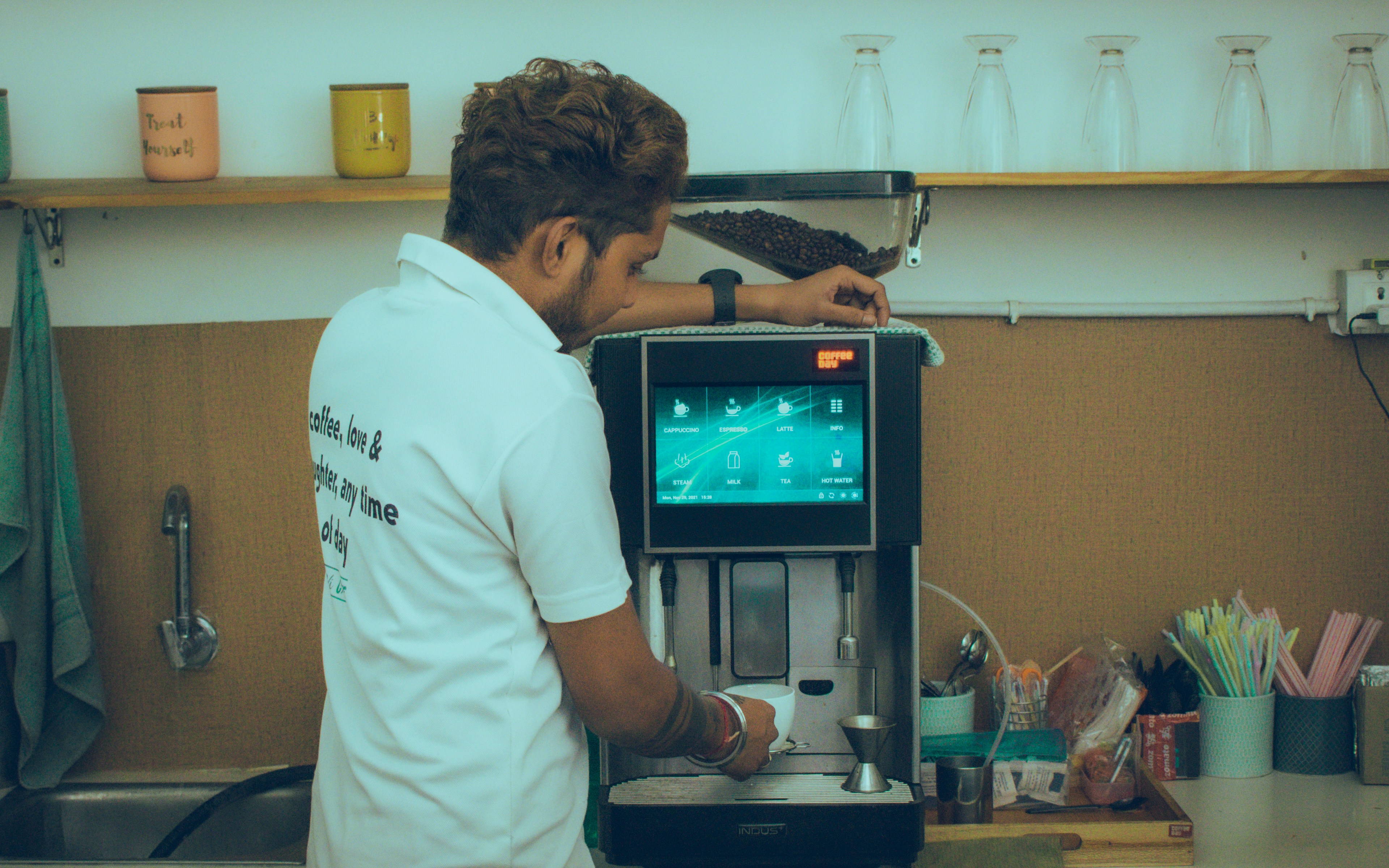 Barista operating a modern beverage dispenser in a cozy café setting, surrounded by colorful utensils and ingredients.