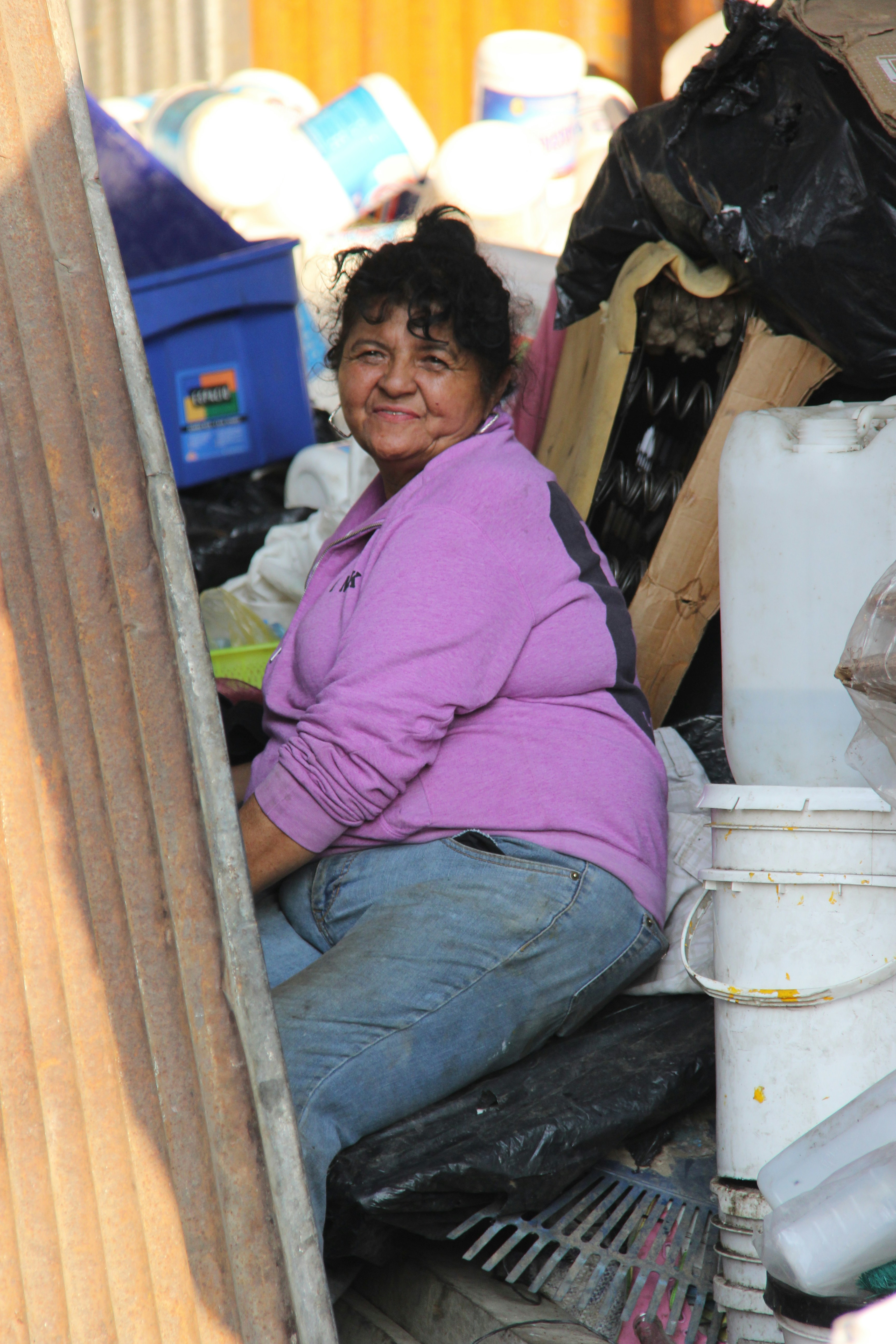 Woman in a Purple Hoodie Pauses Among Recycled Drums and Buckets