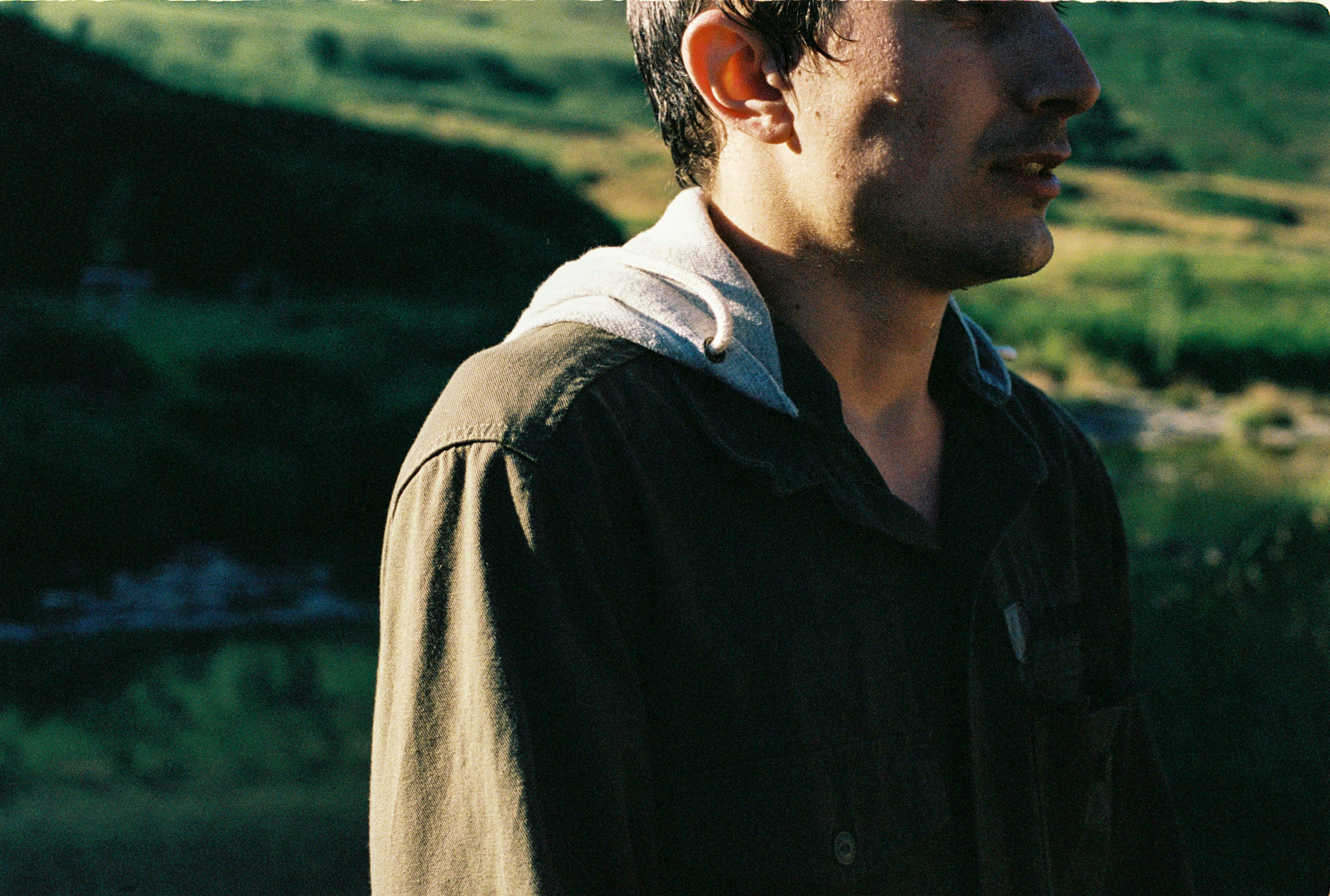 Person in a green jacket standing against a backdrop of lush rolling hills.