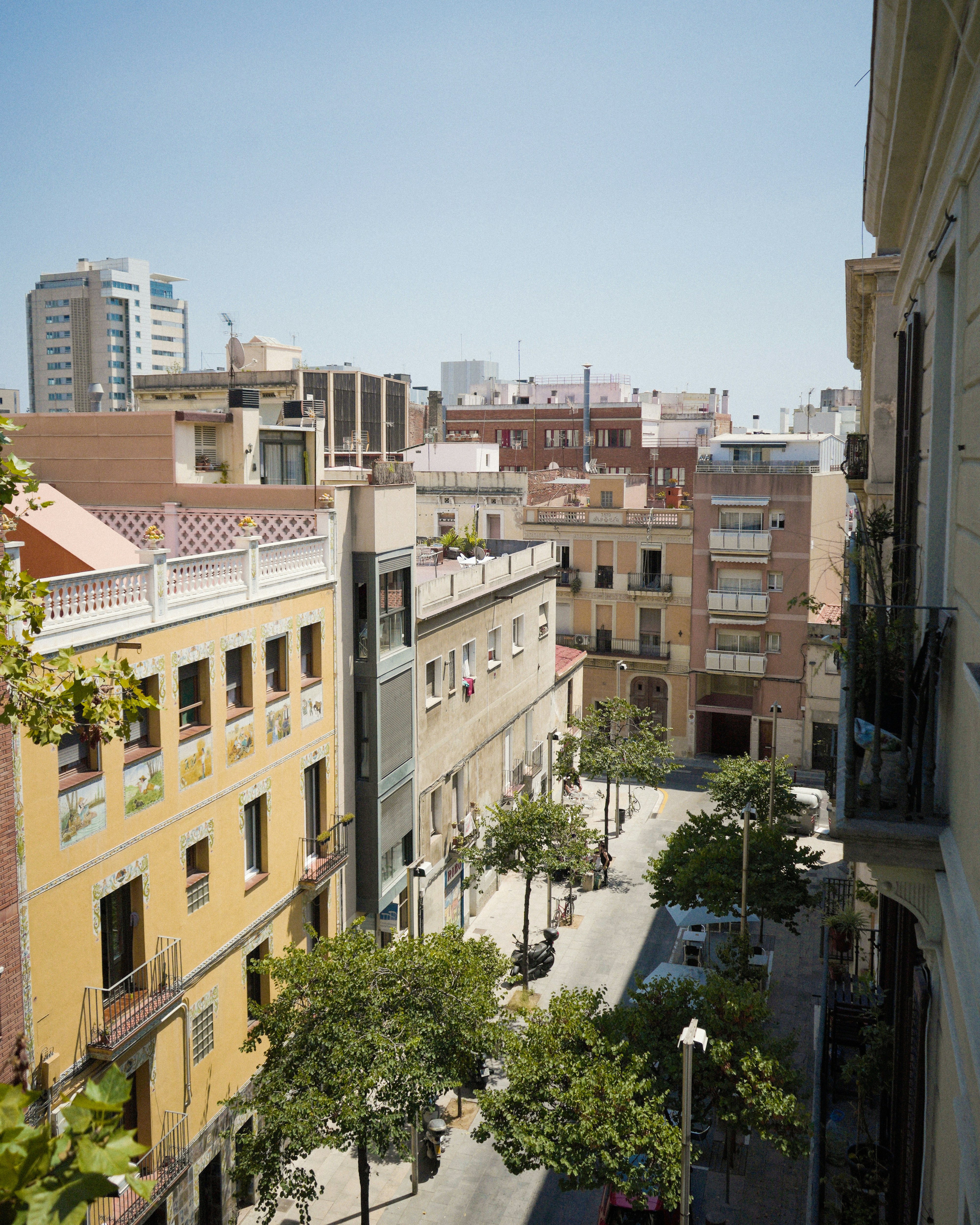 A vibrant cityscape featuring a blend of colorful buildings and lush greenery, showcasing the essence of urban living. The scene captures a sunlit street filled with trees and balconies.