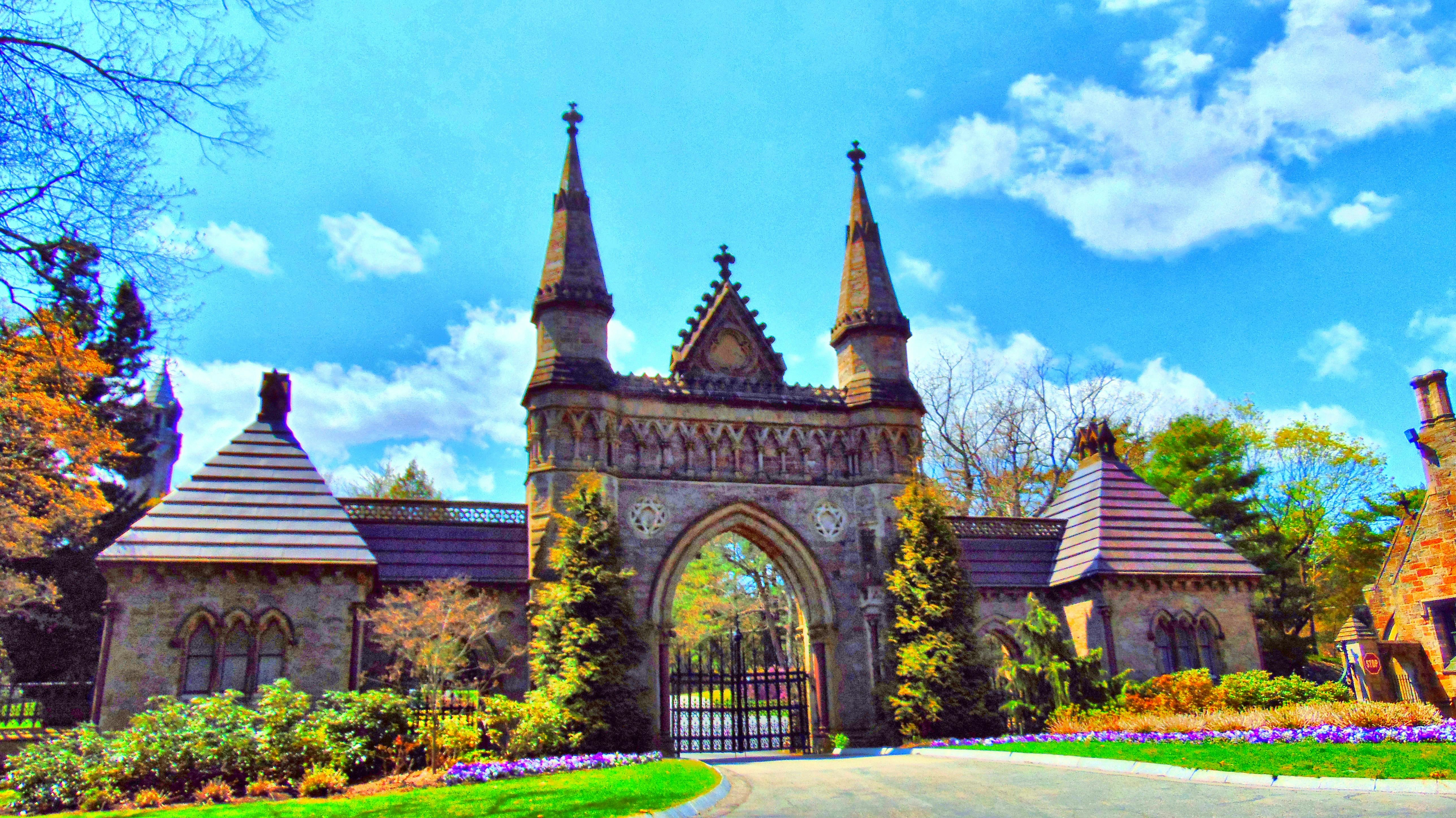 Intricate stone archway framed by lush greenery and vibrant flowers, inviting exploration into a historic site.