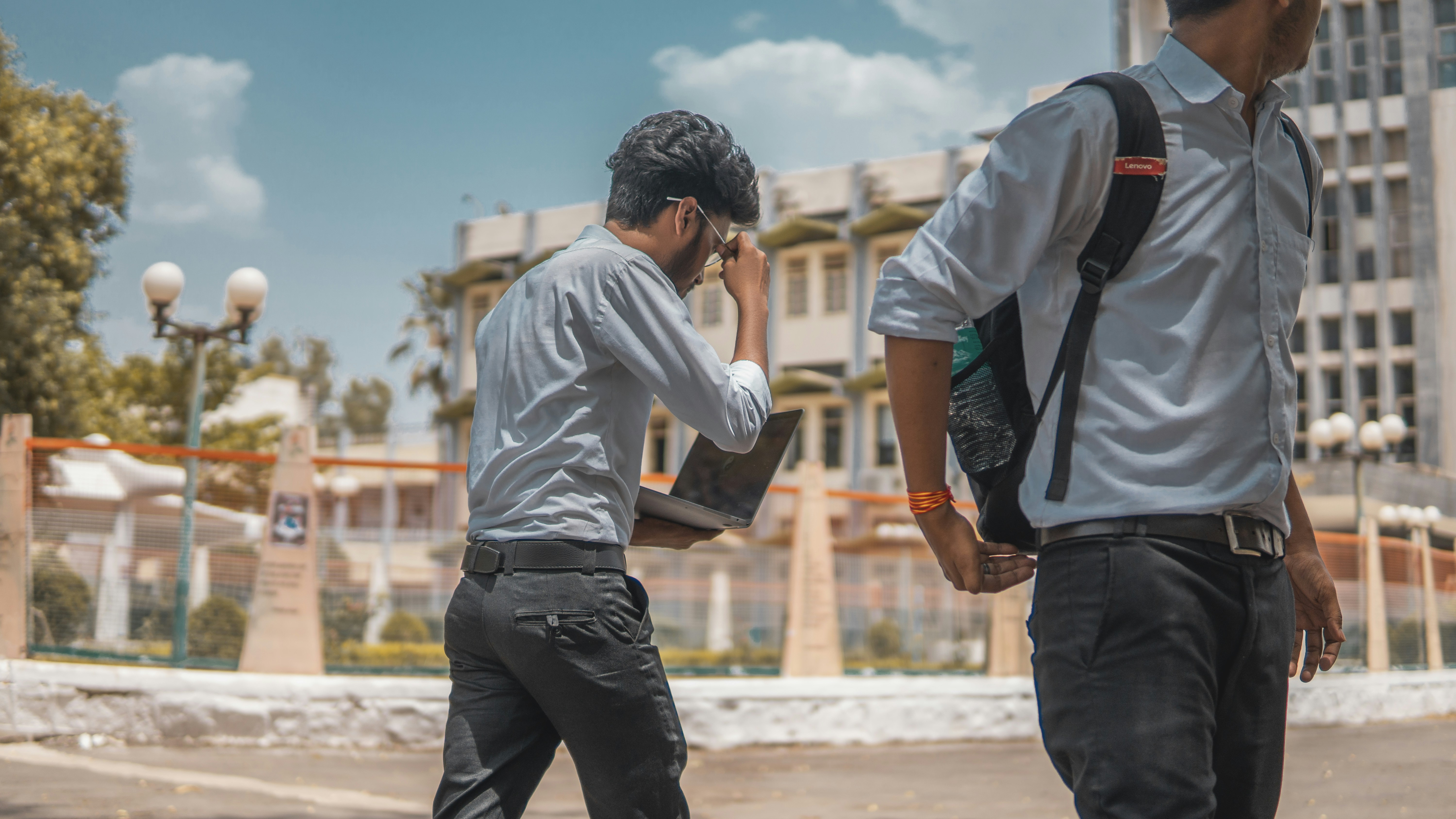 Two students walking through a sunlit campus with modern architecture in the background.
