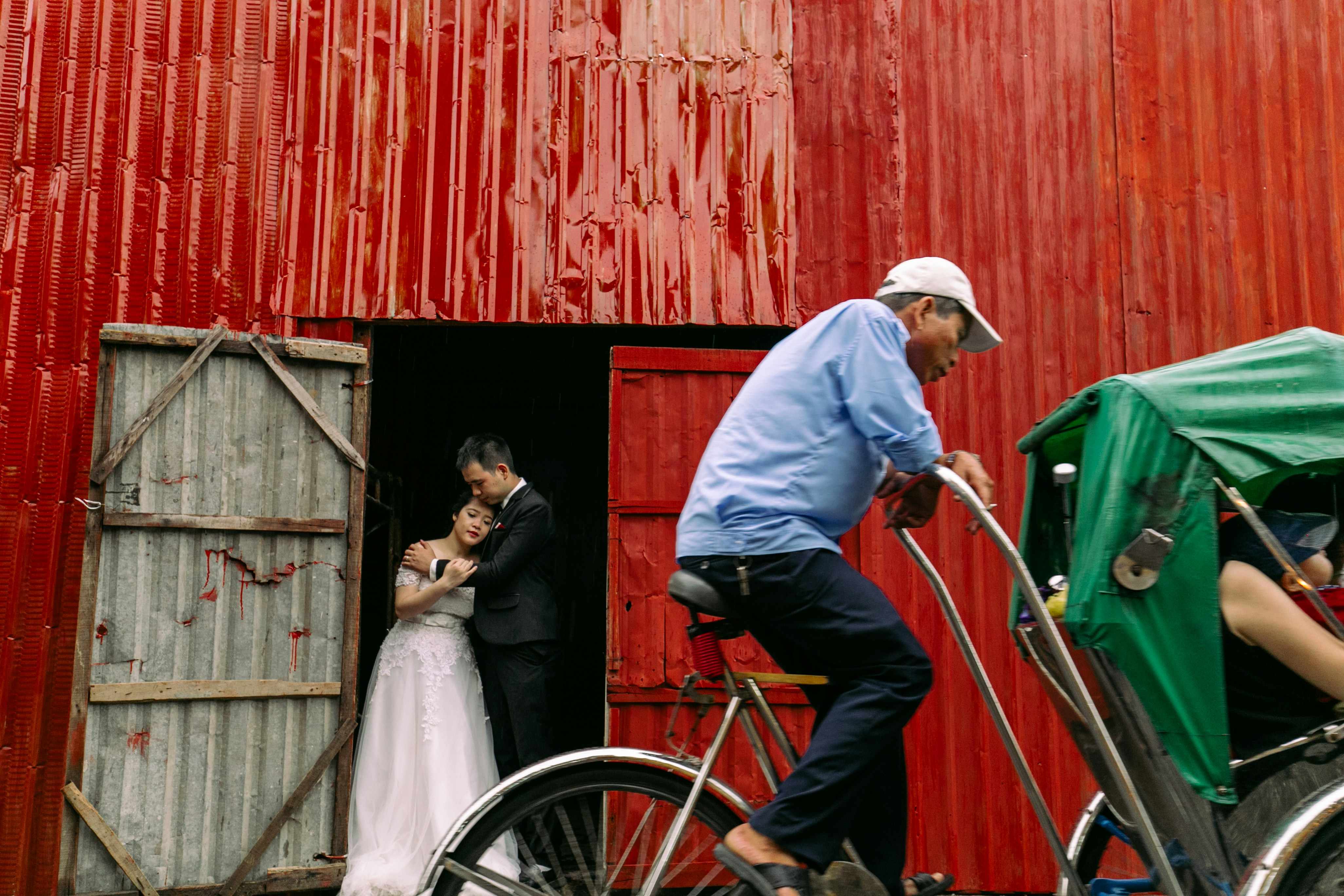 Vows Behind the Scarlet Wall: A Wedding Moment Framed by a Passing Cyclist
