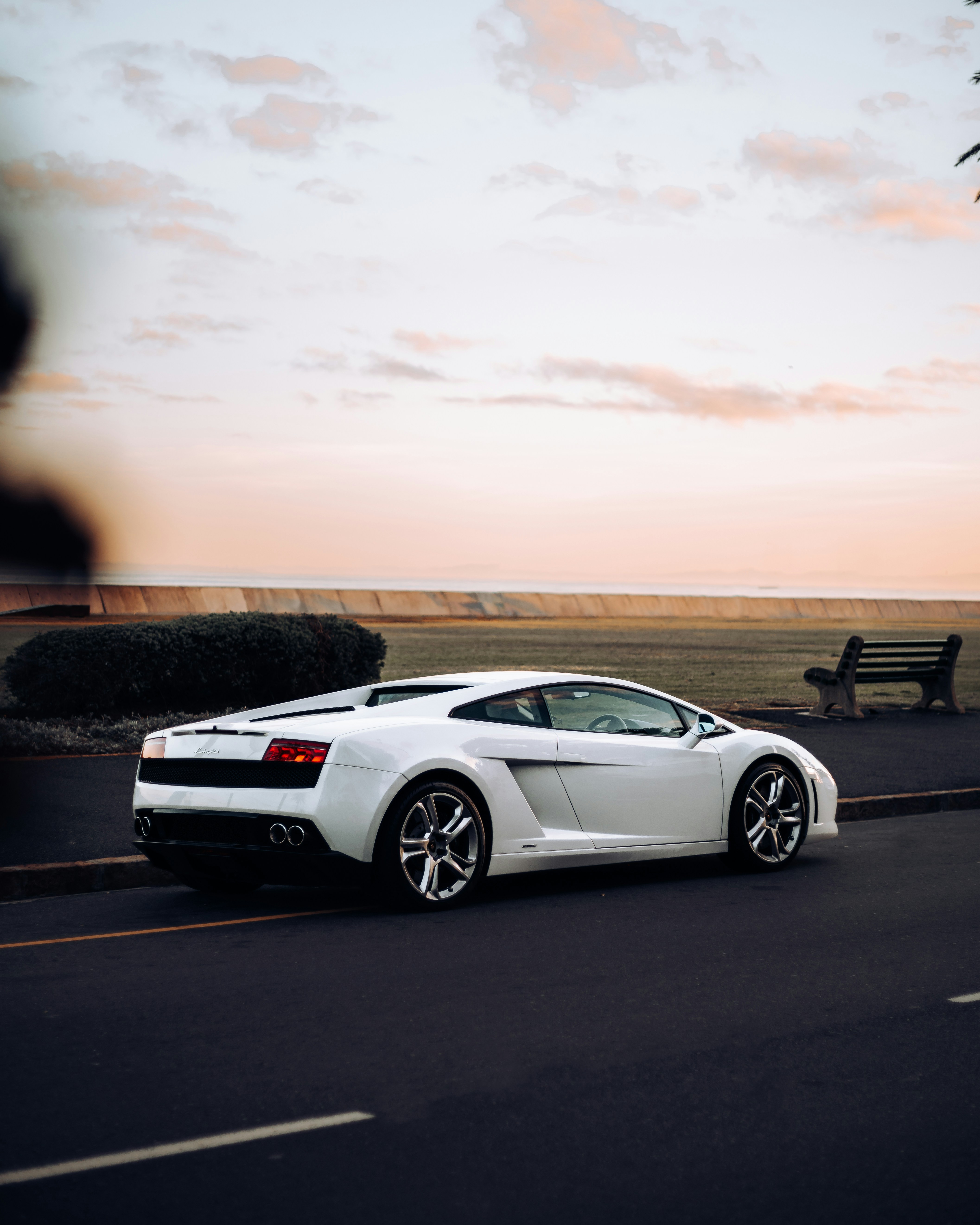 Sleek white sports car parked along a scenic waterfront road at dusk, with a soft pastel sky in the background.
