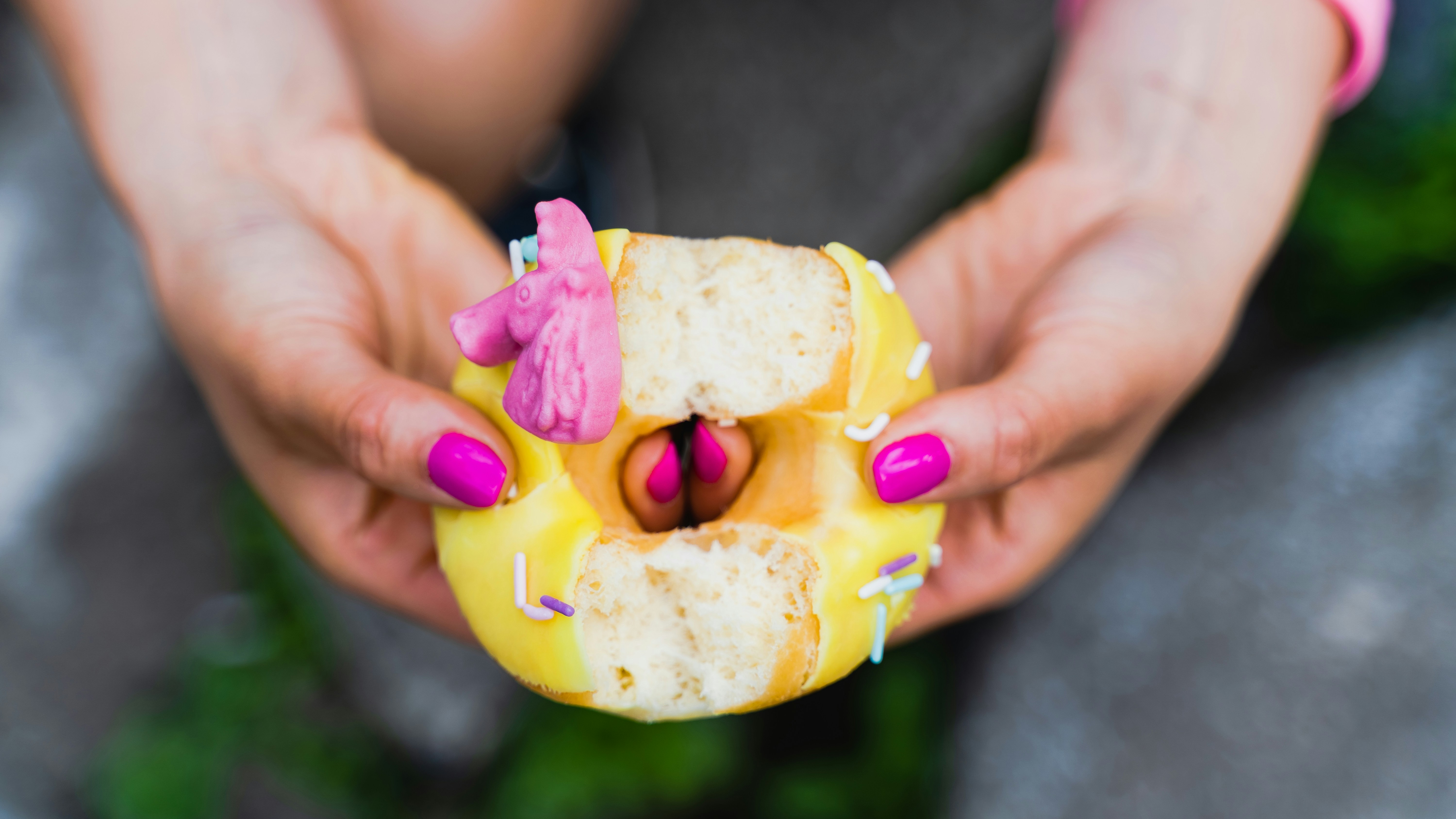 Candy-Drip Moment: Pink-Nailed Hands Cradle a Yellow-Glazed Donut