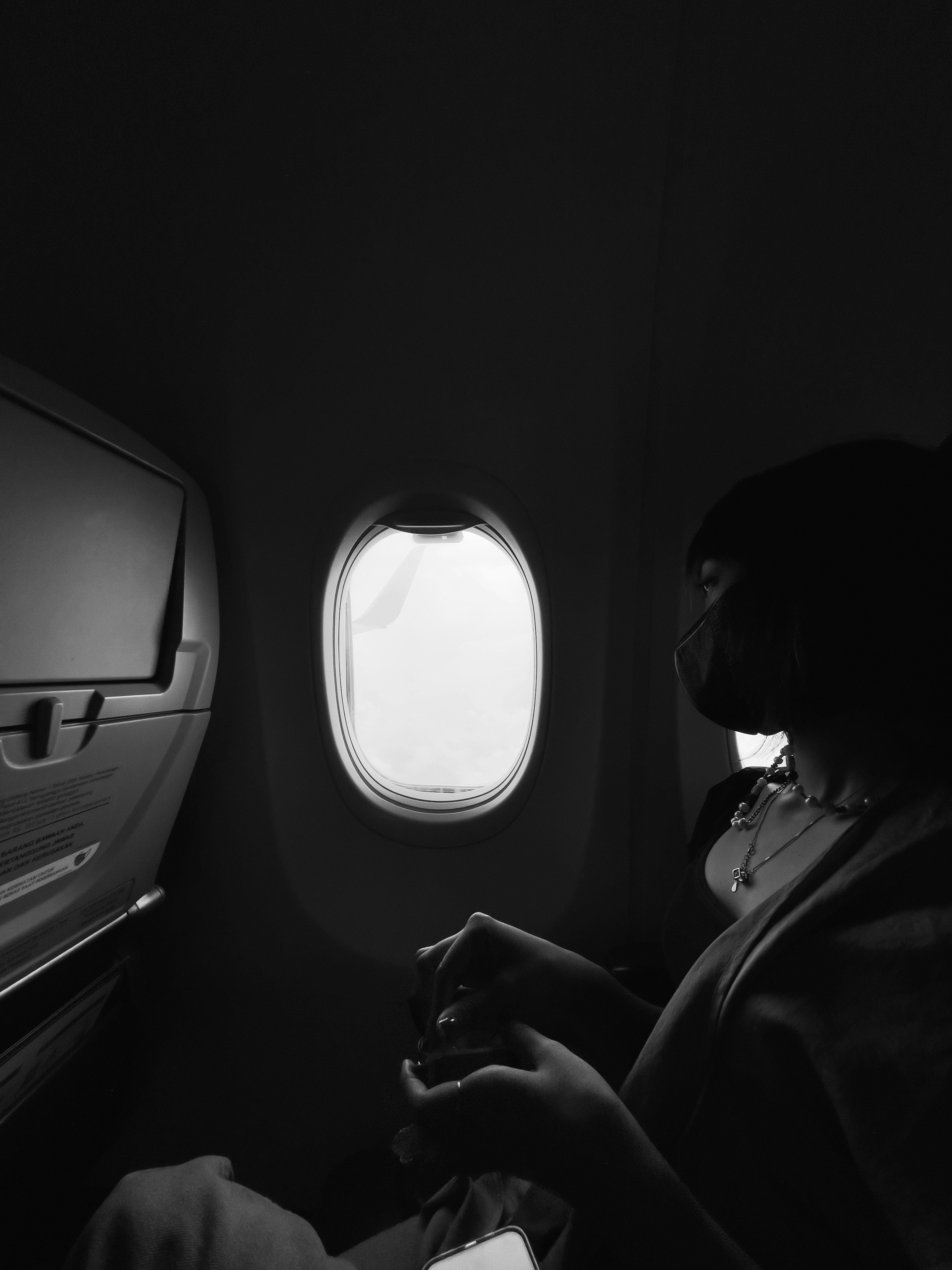 A traveler gazing out the airplane window, lost in thought, as clouds drift by. The scene captures a moment of reflection amidst the journey.