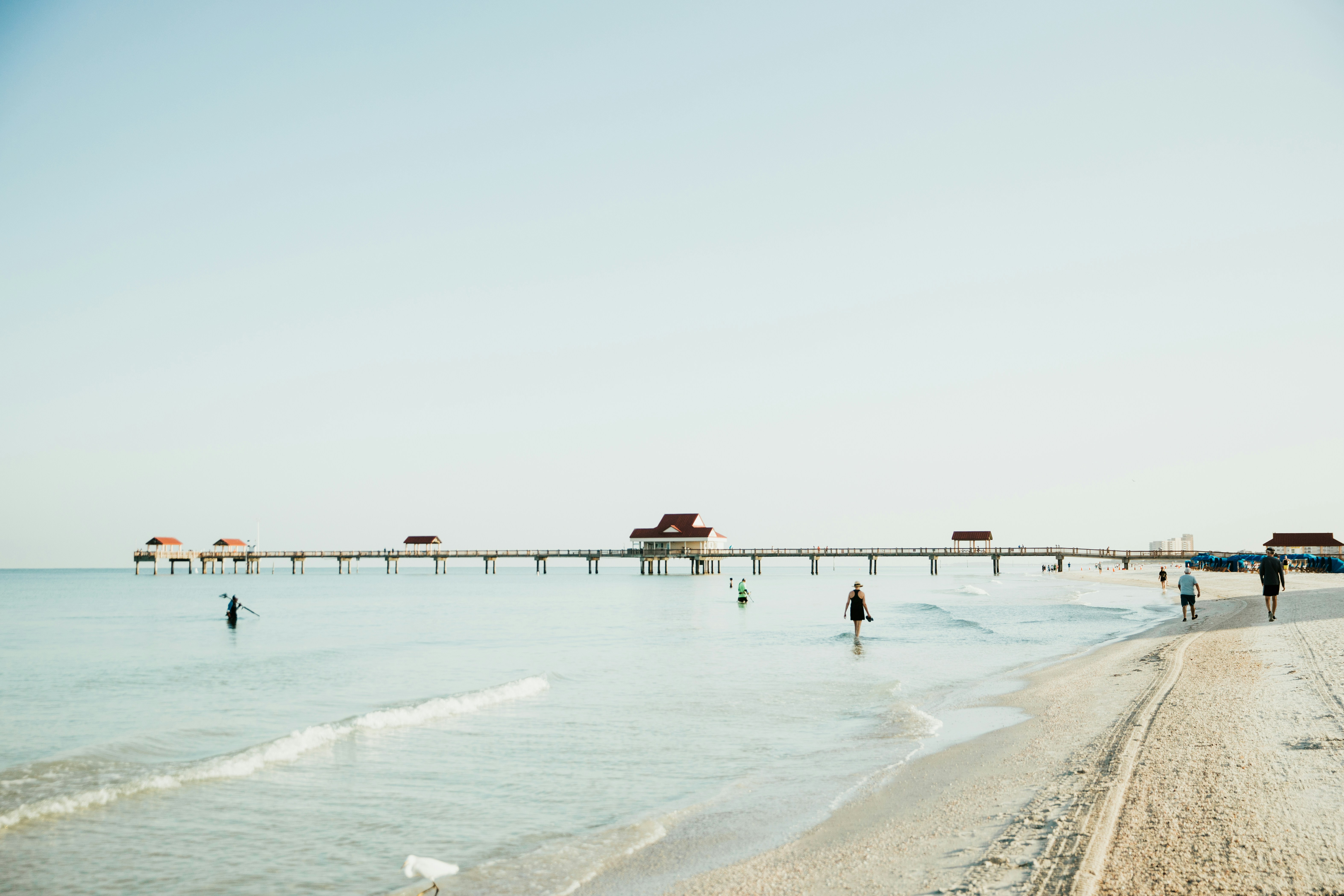 Long pier stretching into calm sea under a clear sky, with gentle waves lapping at sandy beach.