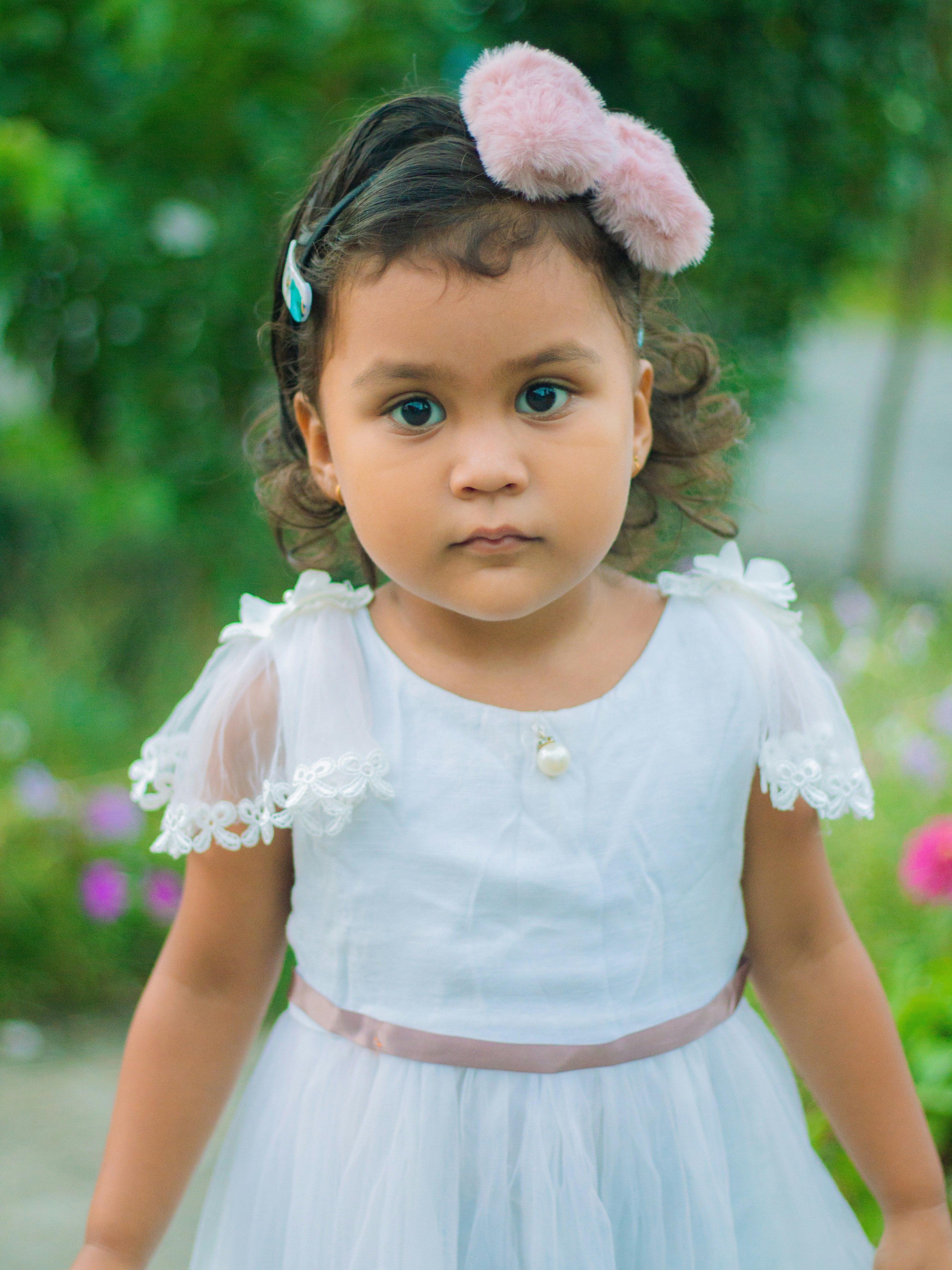 A little girl wearing a white dress and a pink flower in her hair photo ...