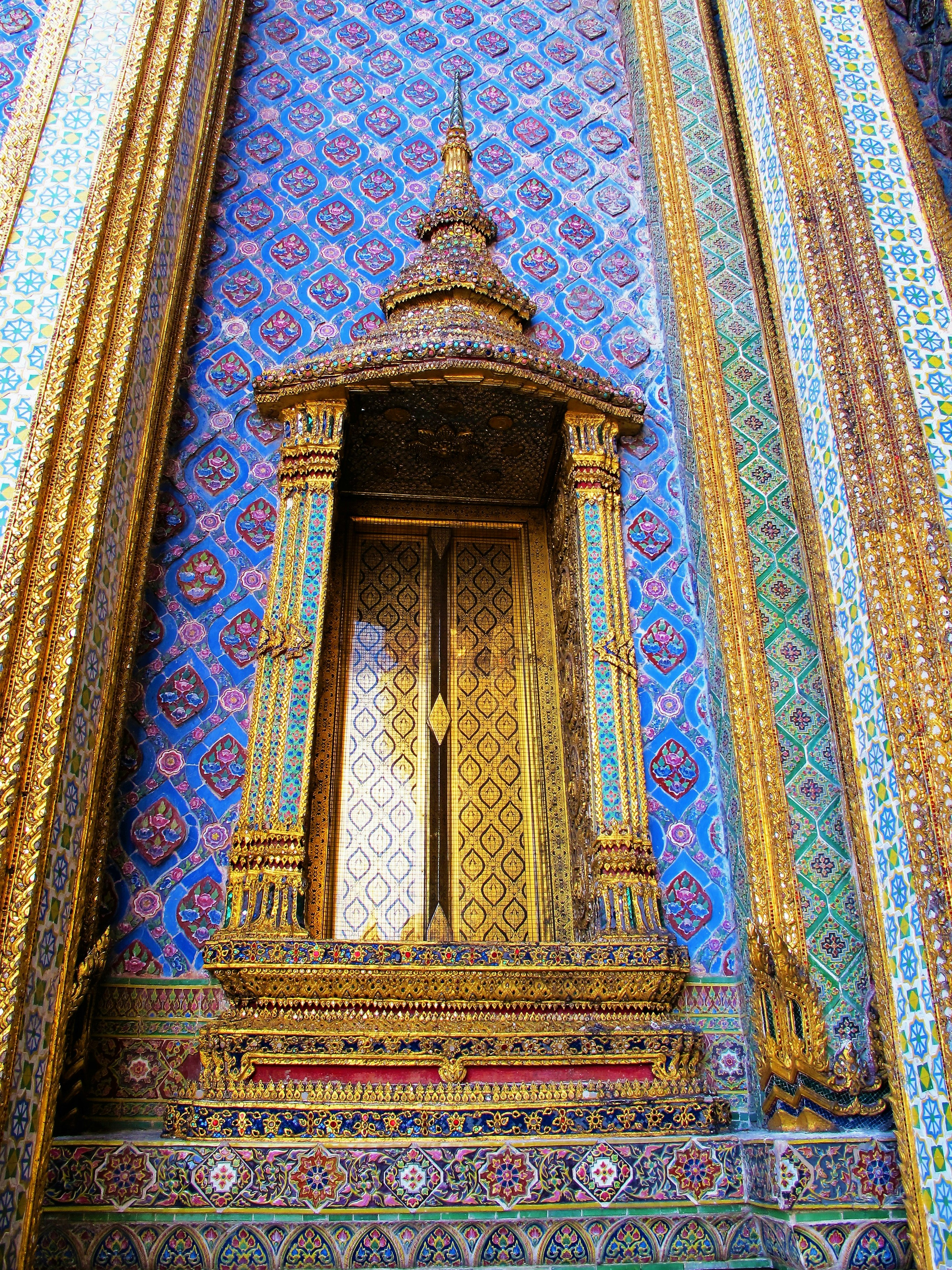 Photograph shows a gilded temple doorway framed by cerulean blue tilework and ornate columns.