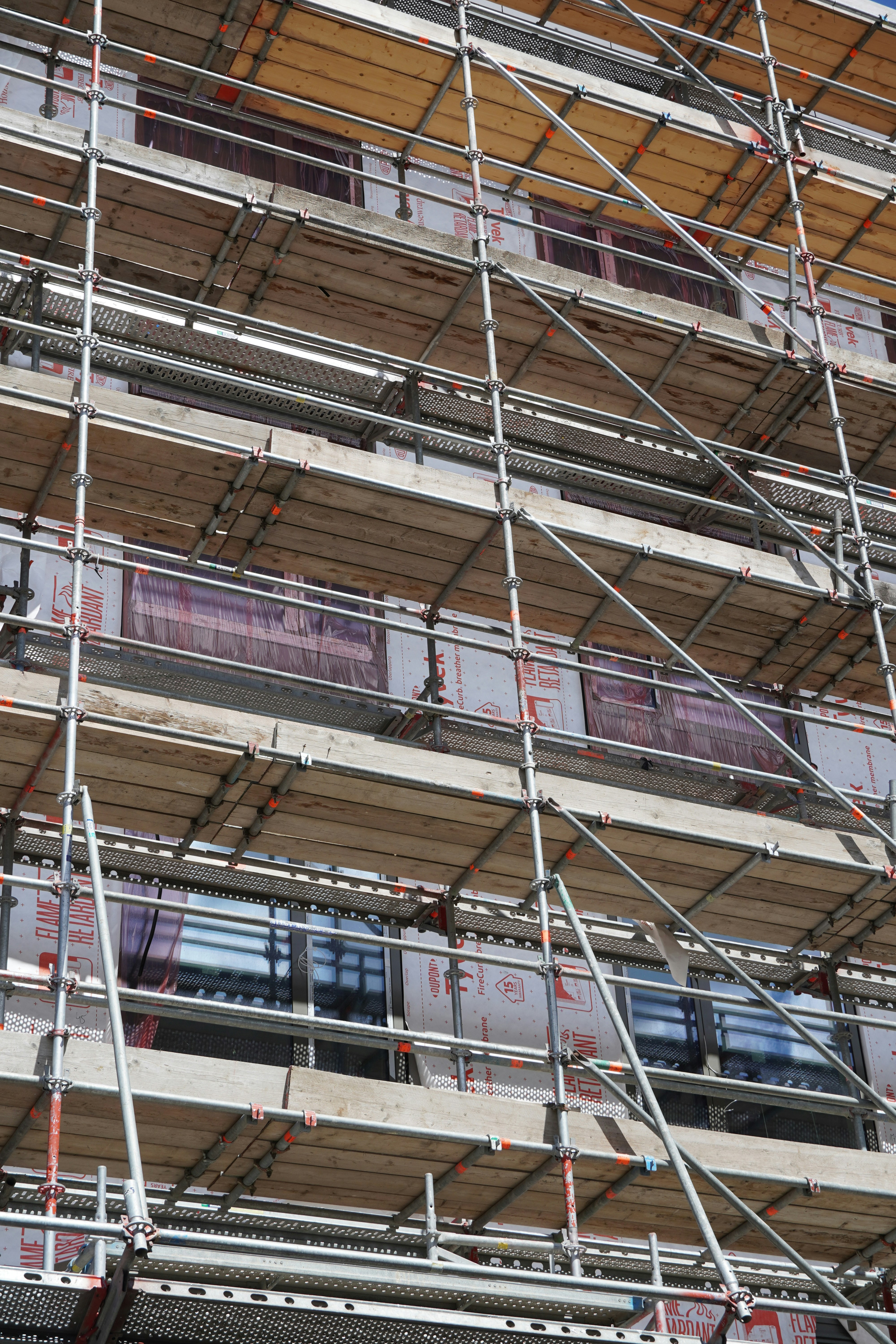 Scaffolding enveloping a building under renovation, showcasing layers of wood and protective sheeting. The scene captures the essence of urban development.