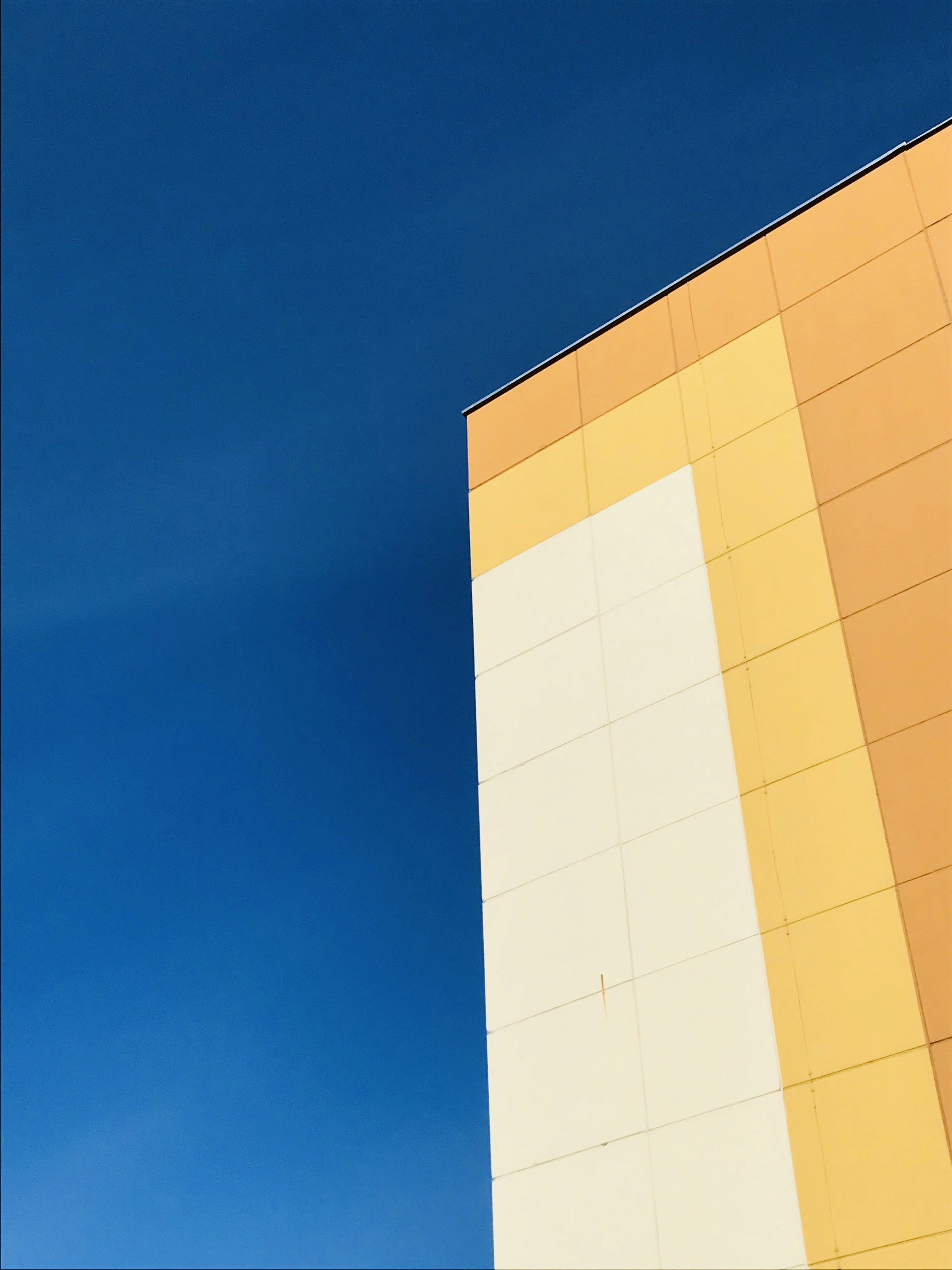 A vibrant building corner showcasing a gradient of yellow and white panels against a clear blue sky.
