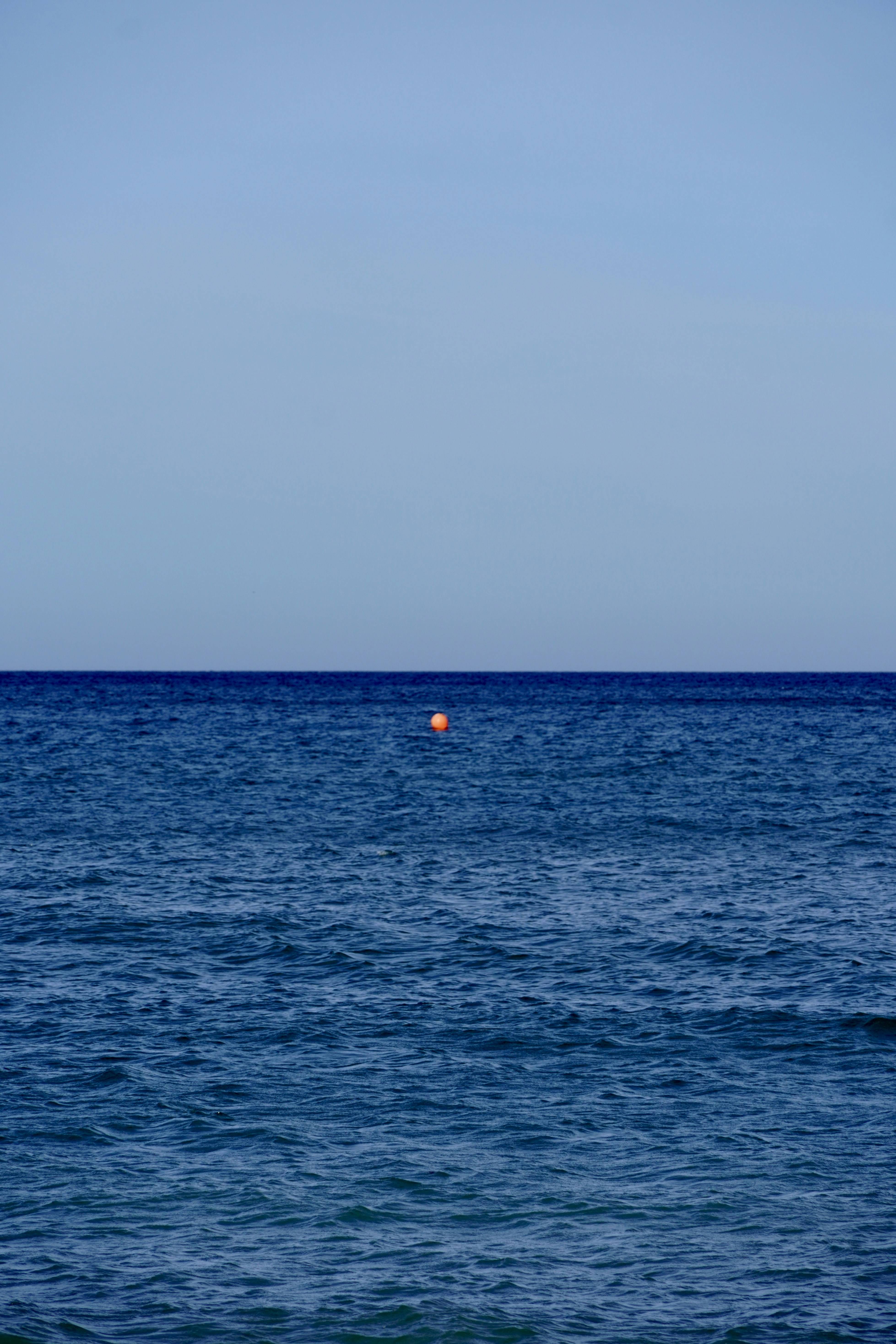 Horizon Sentinel: An Orange Buoy Anchored in a Quiet Blue Sea