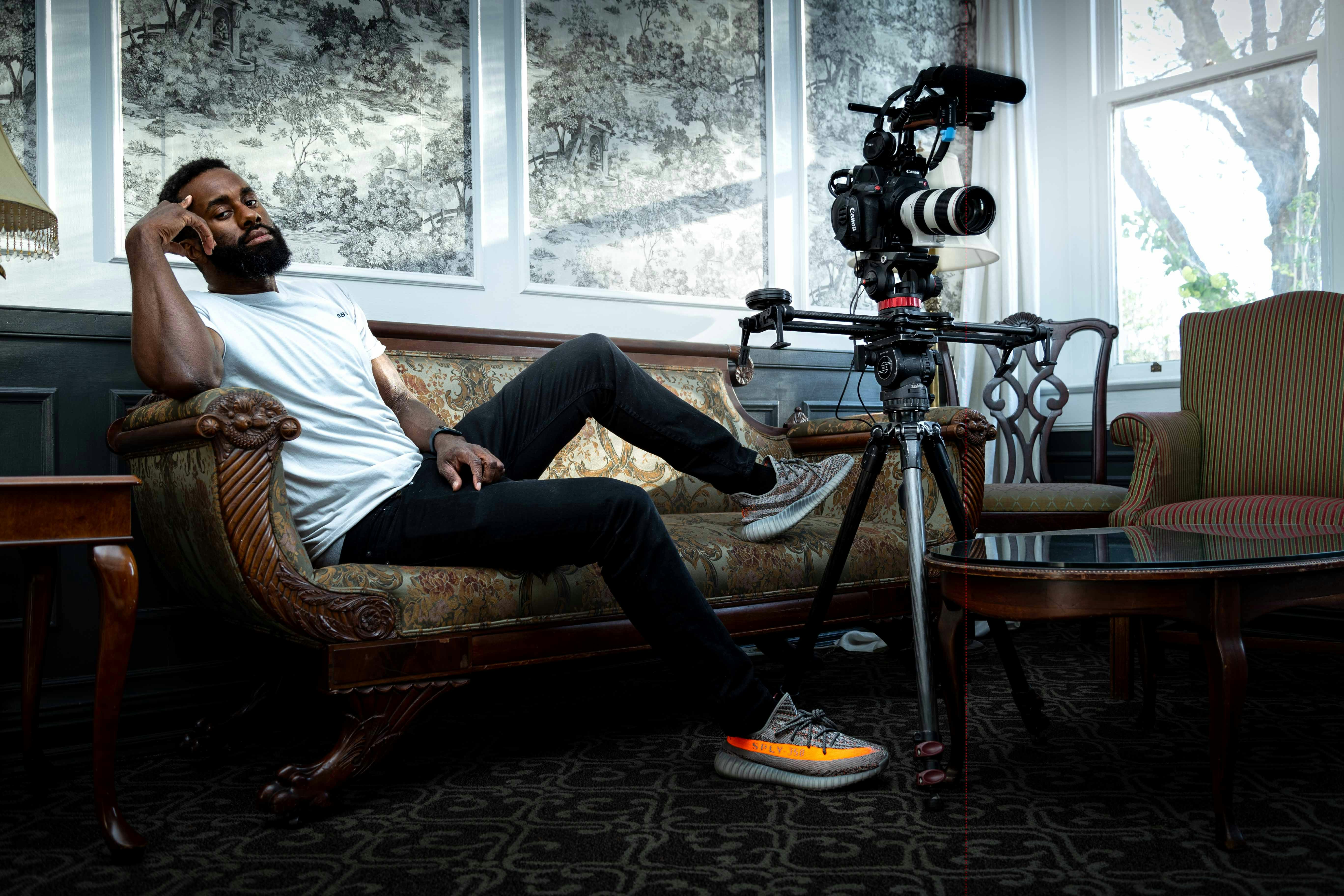 A man sitting on a couch next to a camera photo – Free Camera lens ...