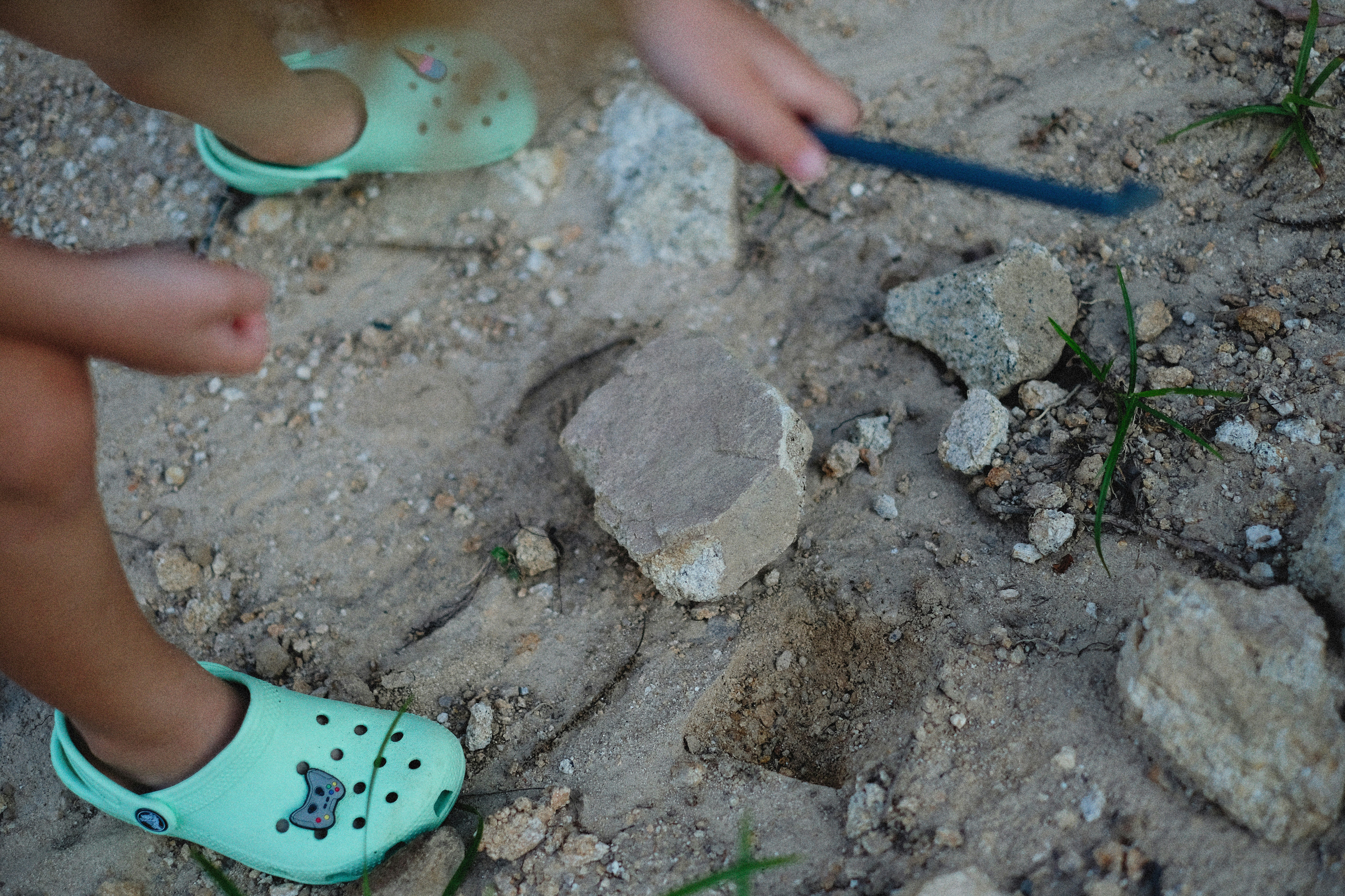 Ground-Level Mosaic: Mint Crocs, Rocks, and a Playful Blue Stick