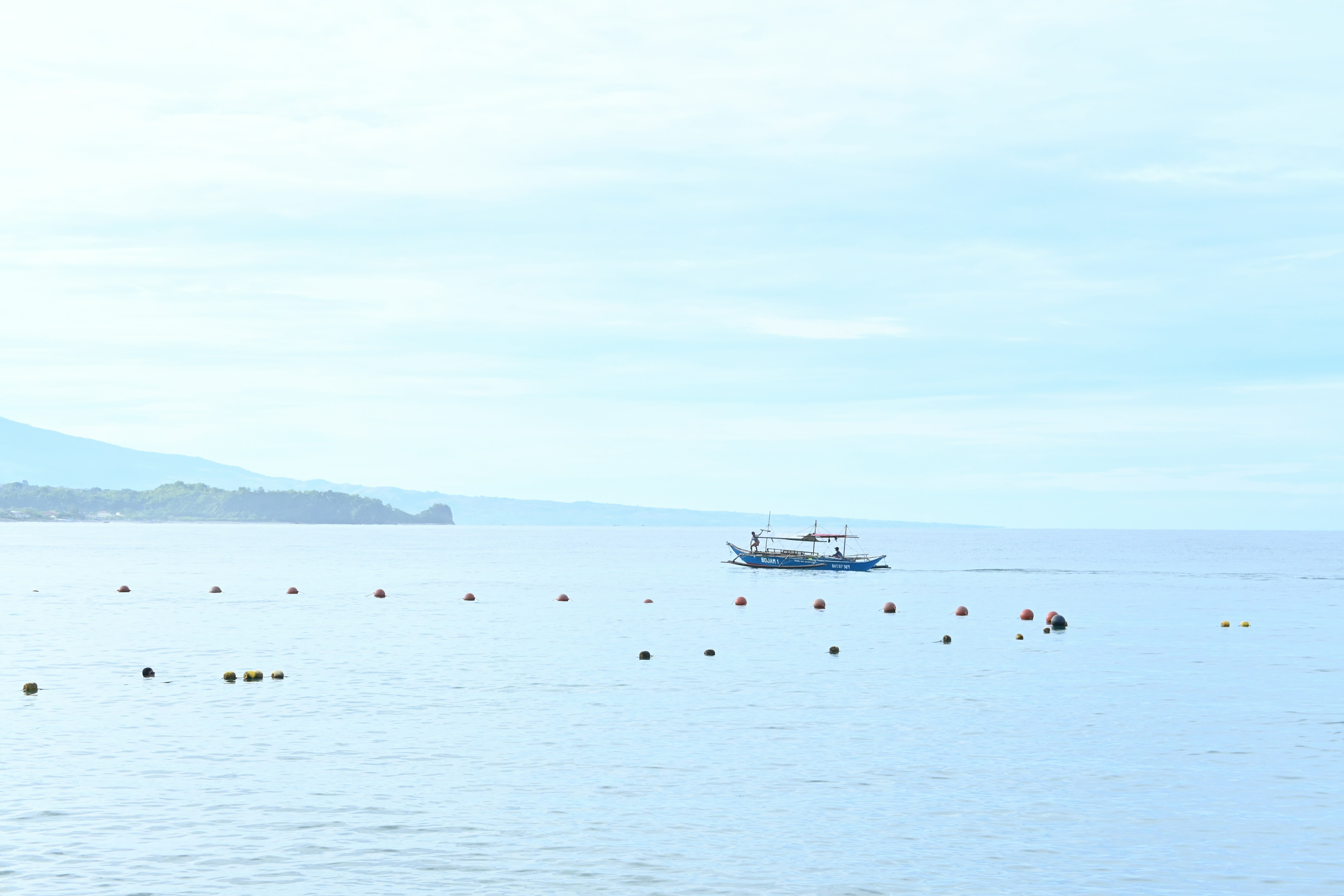 Boat floating on calm, expansive sea under a pale blue sky.