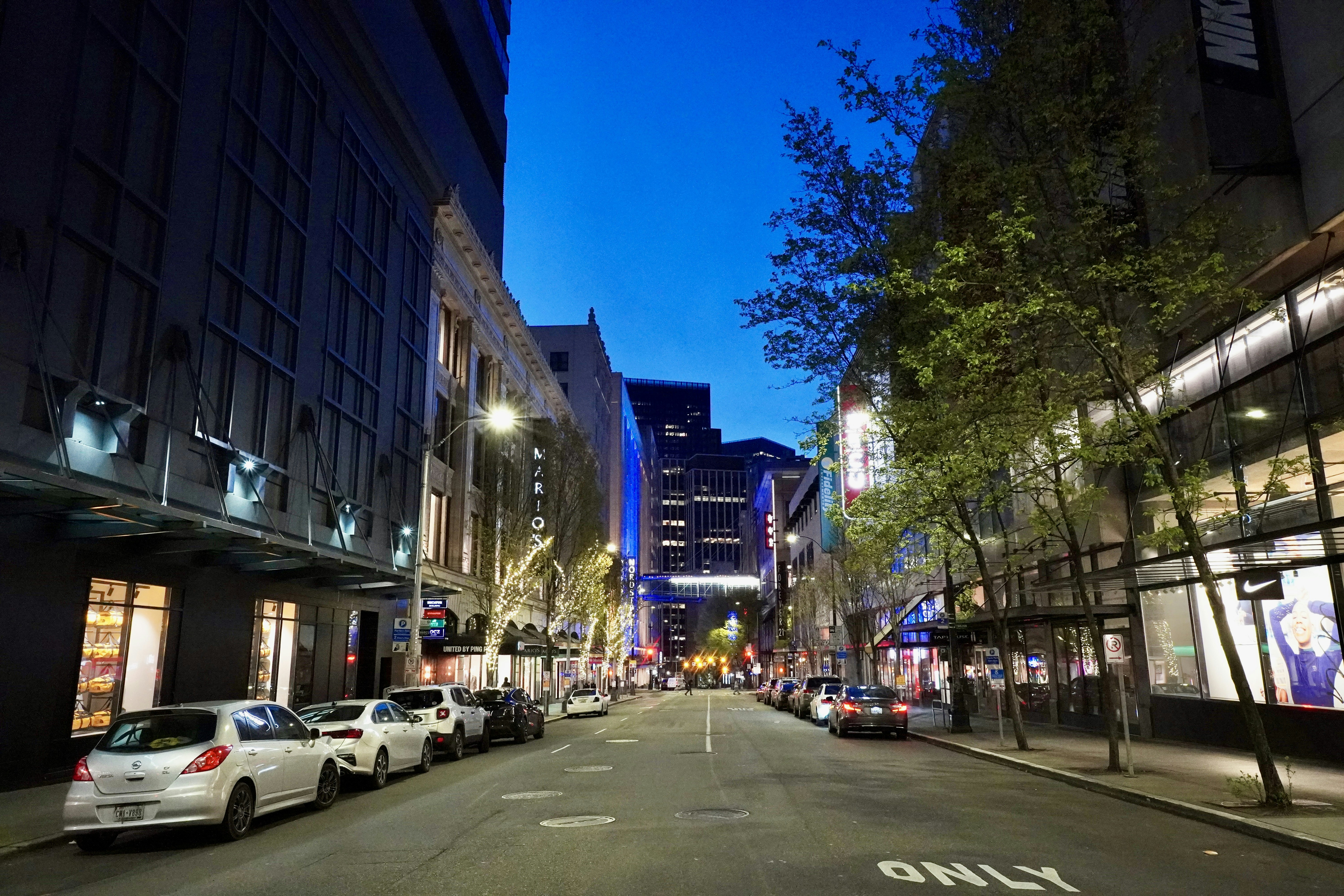 Seattle's Westlake Avenue at night with illuminated retail stores and parked cars under a deep blue sky.
