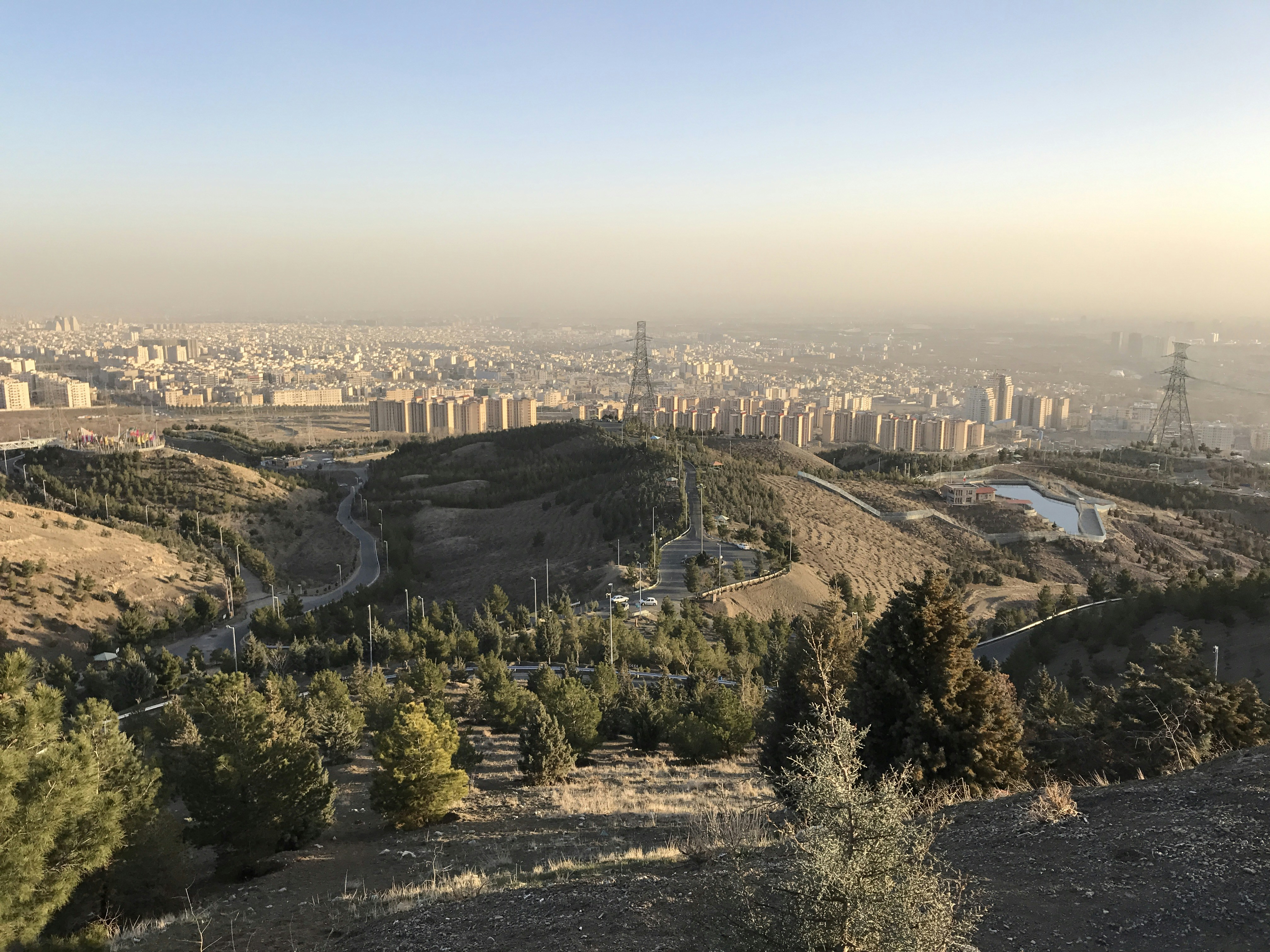 Panoramic view of a sprawling cityscape nestled among rolling hills, showcasing a blend of urban architecture and natural terrain.